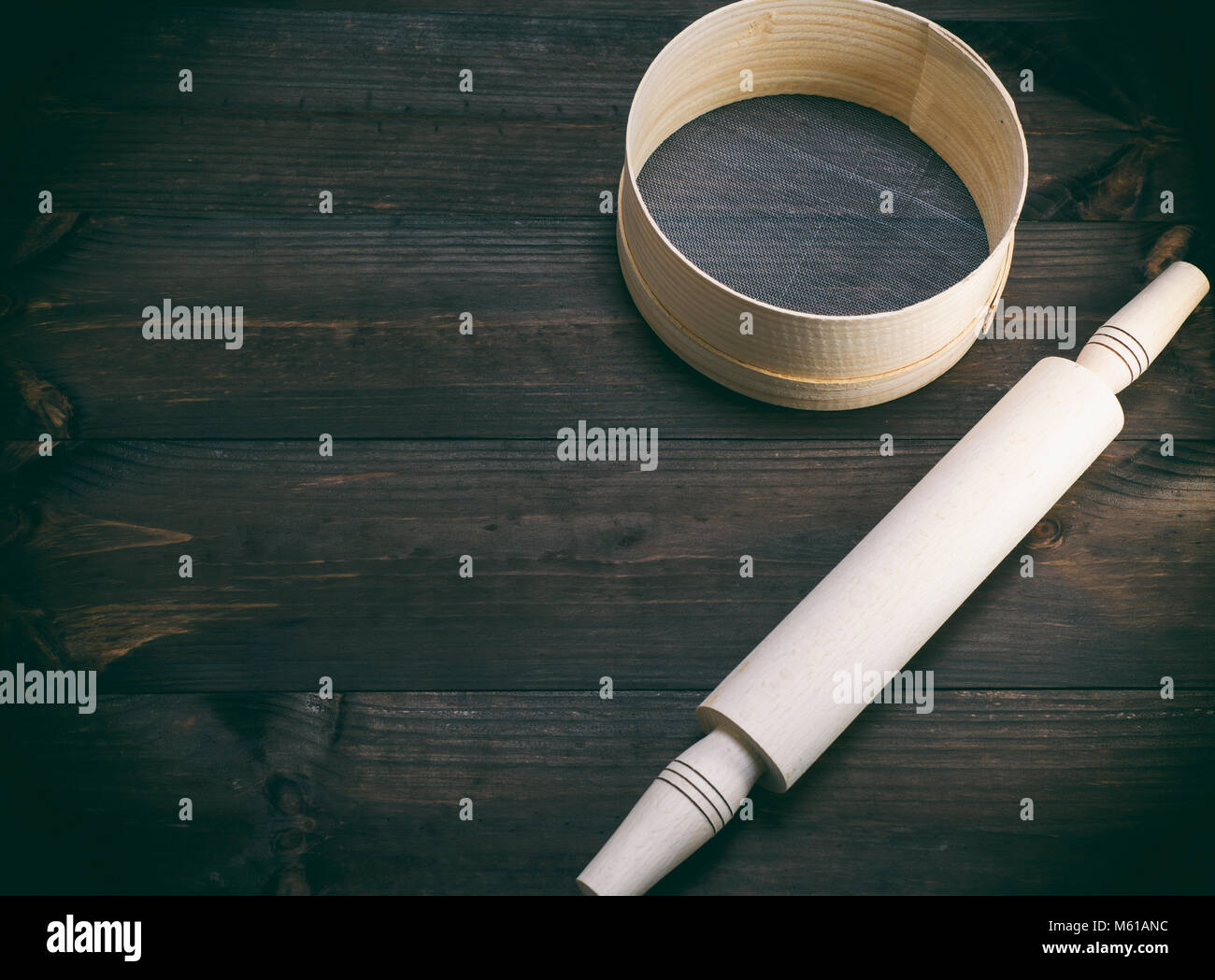 wooden rolling pin and a wooden round sieve on a brown table, top view ...