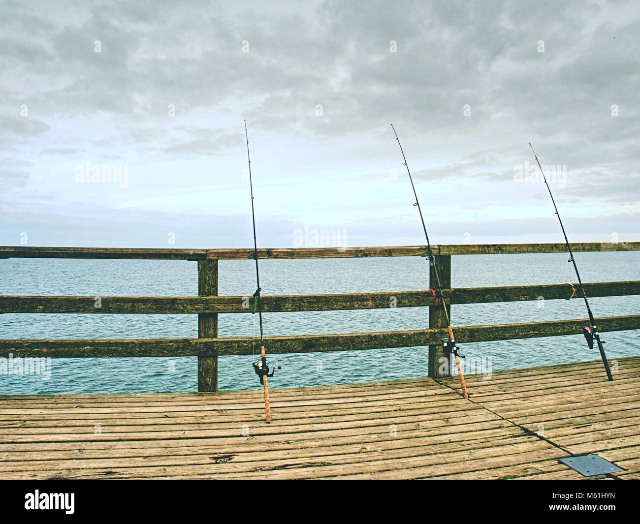 Fishers rods against handrail of wooden bridge. Fishing on harbor mole ...