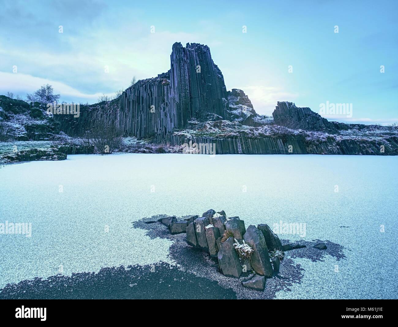 Peak of basalt pillars covered by snow, frozen pool. Full moon in blue ...