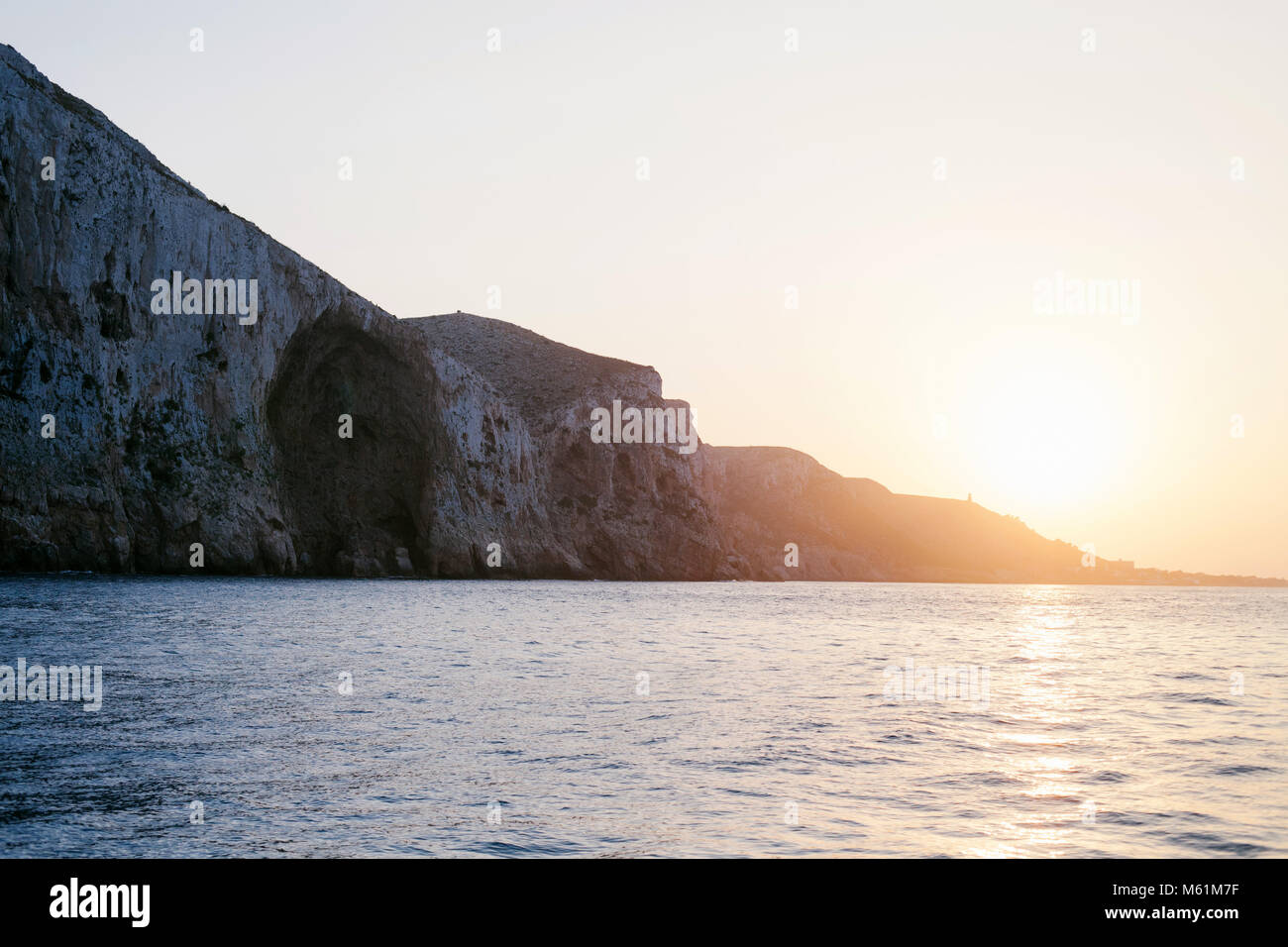 Bright sun setting over rocky cliffs and calm surface of sea Stock ...