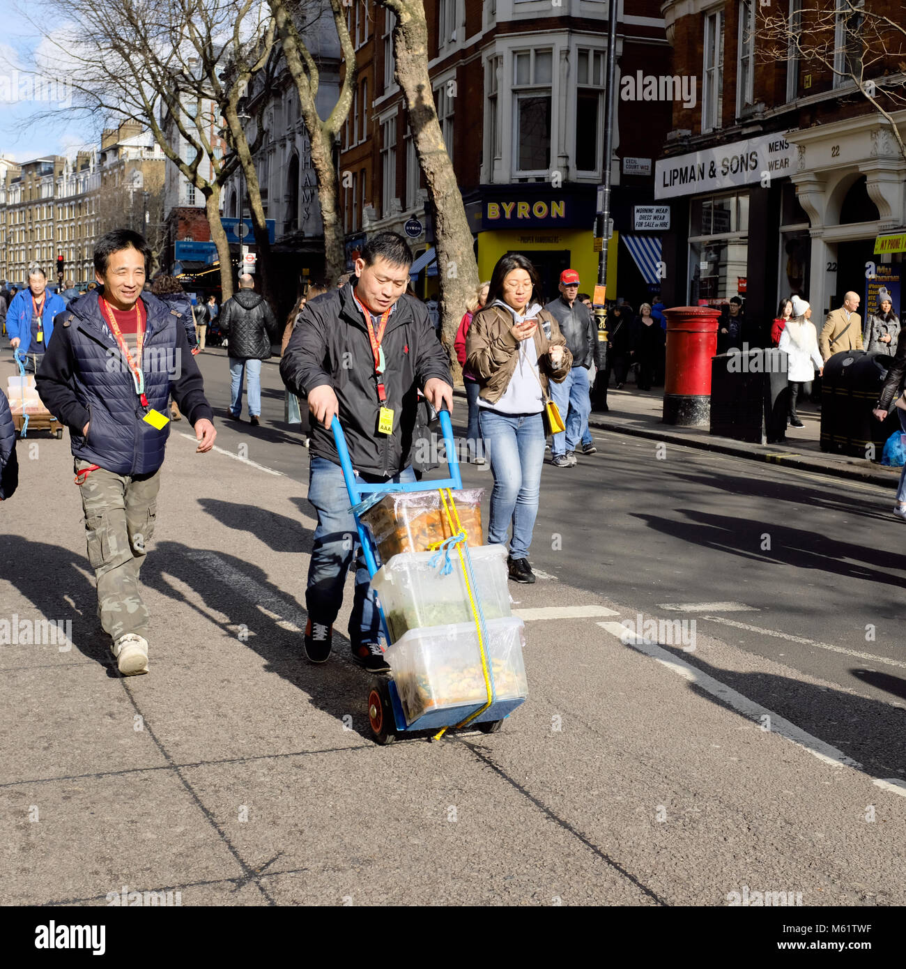 Chinese man pushing a cart stacked with containers of cooked food ...