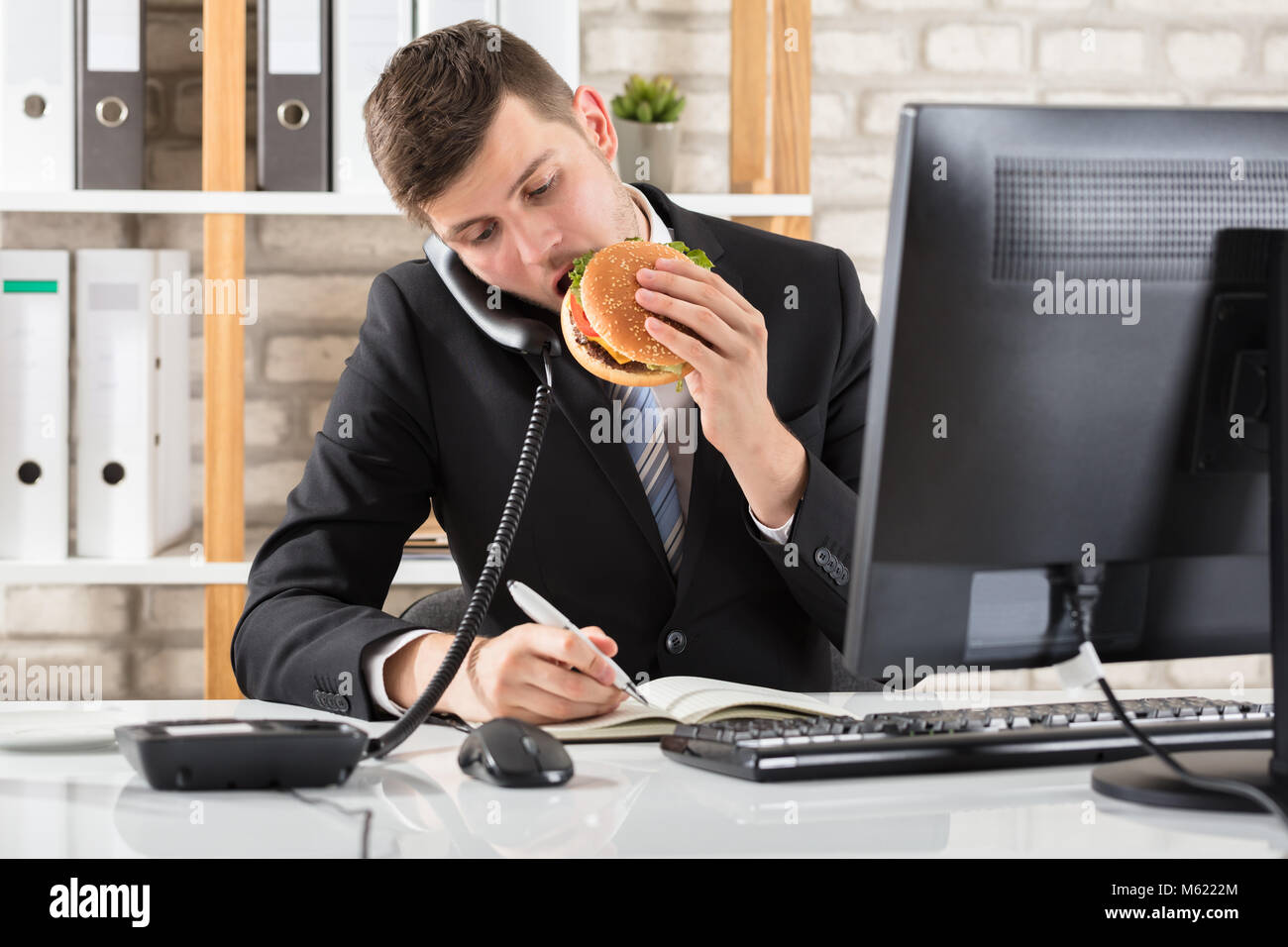 Young Business Man At Desk Eating Burger And Working At Workplace Stock ...