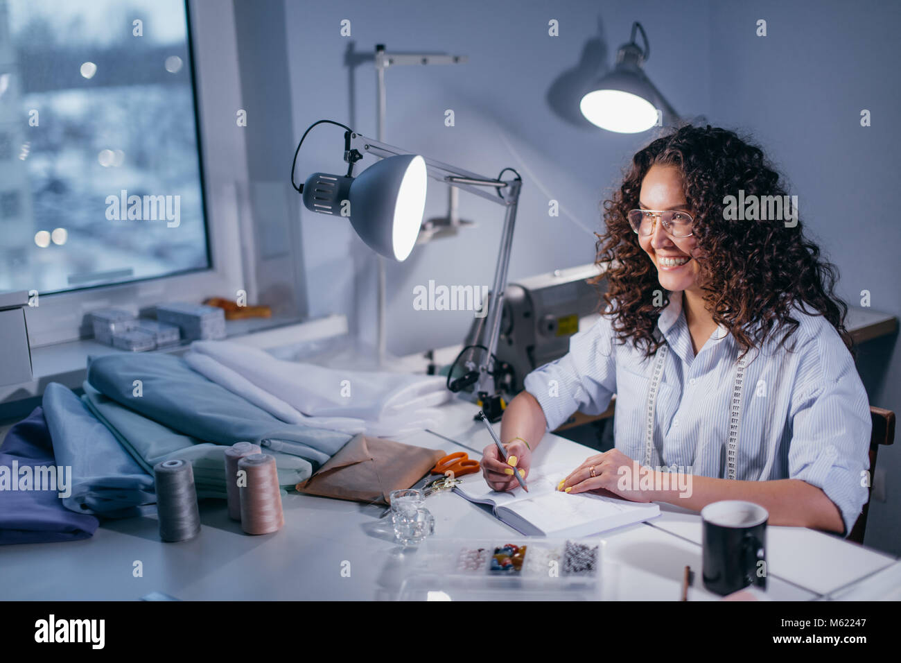 laughing woman writing notes at tailor's table in the evening Stock ...
