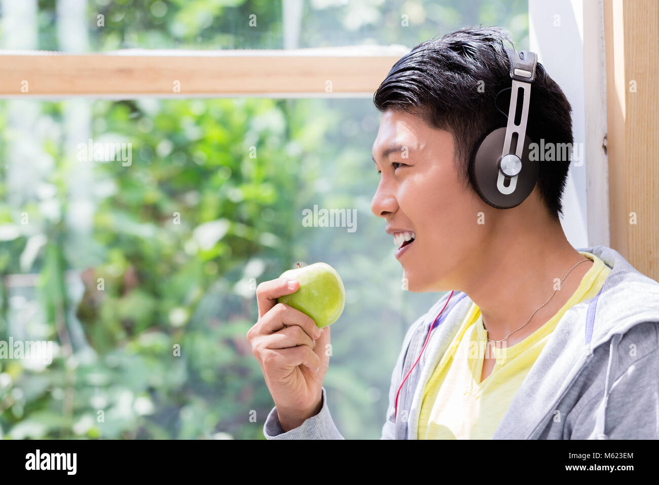 Young man eating a fresh green apple while listening to headphones ...