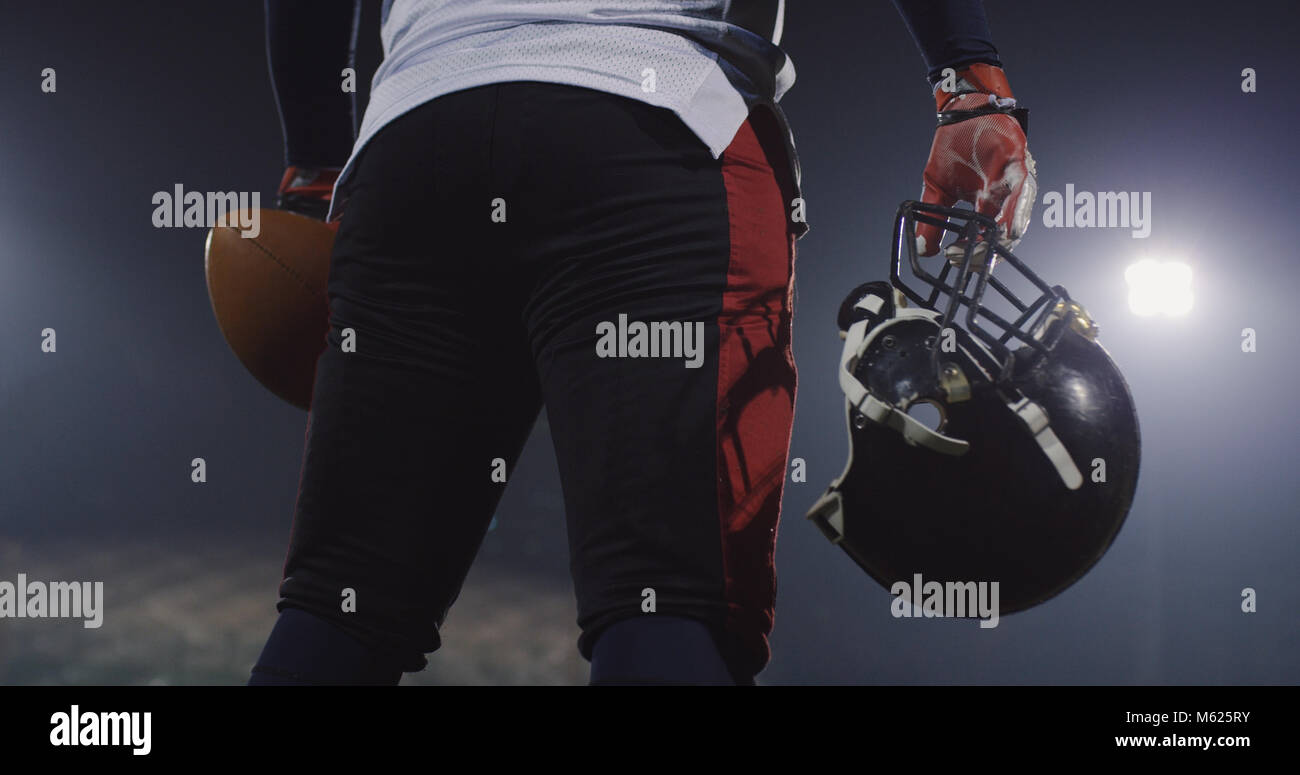portrait of American Football player holding ball and helmet rear view ...