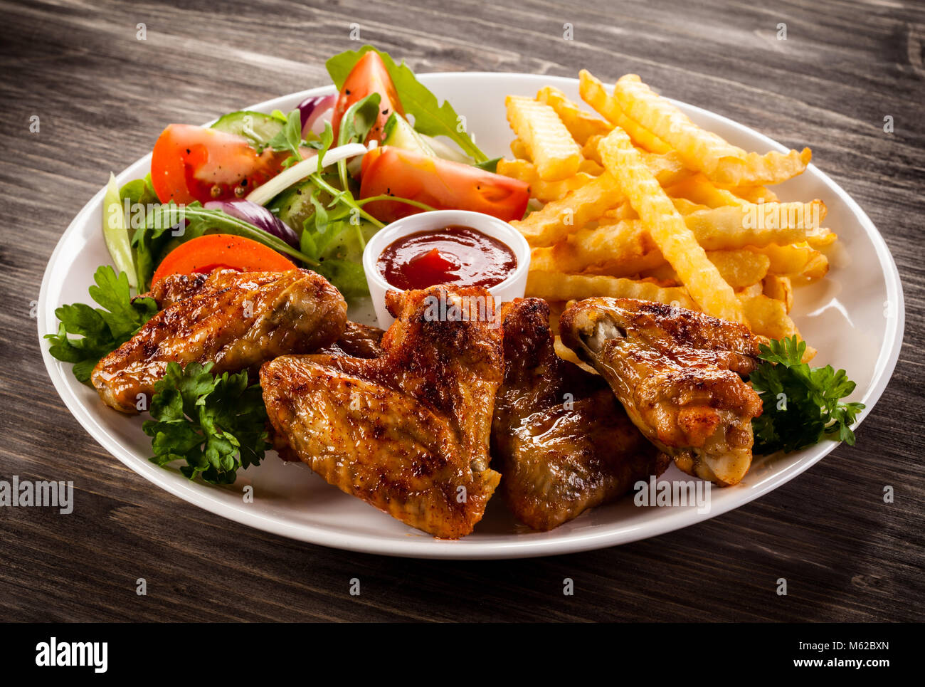 Grilled chicken wigs, chips and vegetables on wooden table Stock Photo ...