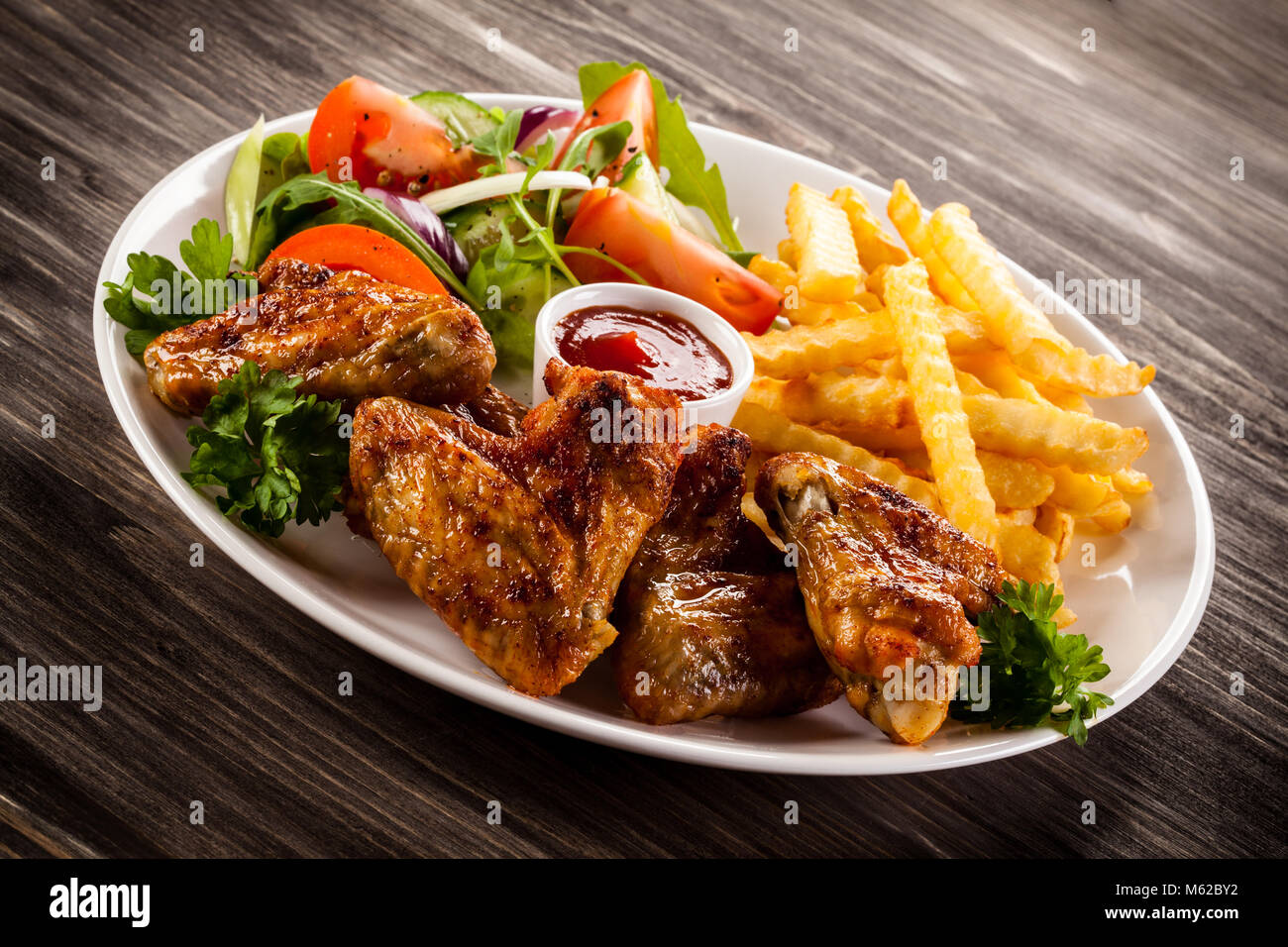 Grilled chicken wigs, chips and vegetables on wooden table Stock Photo ...