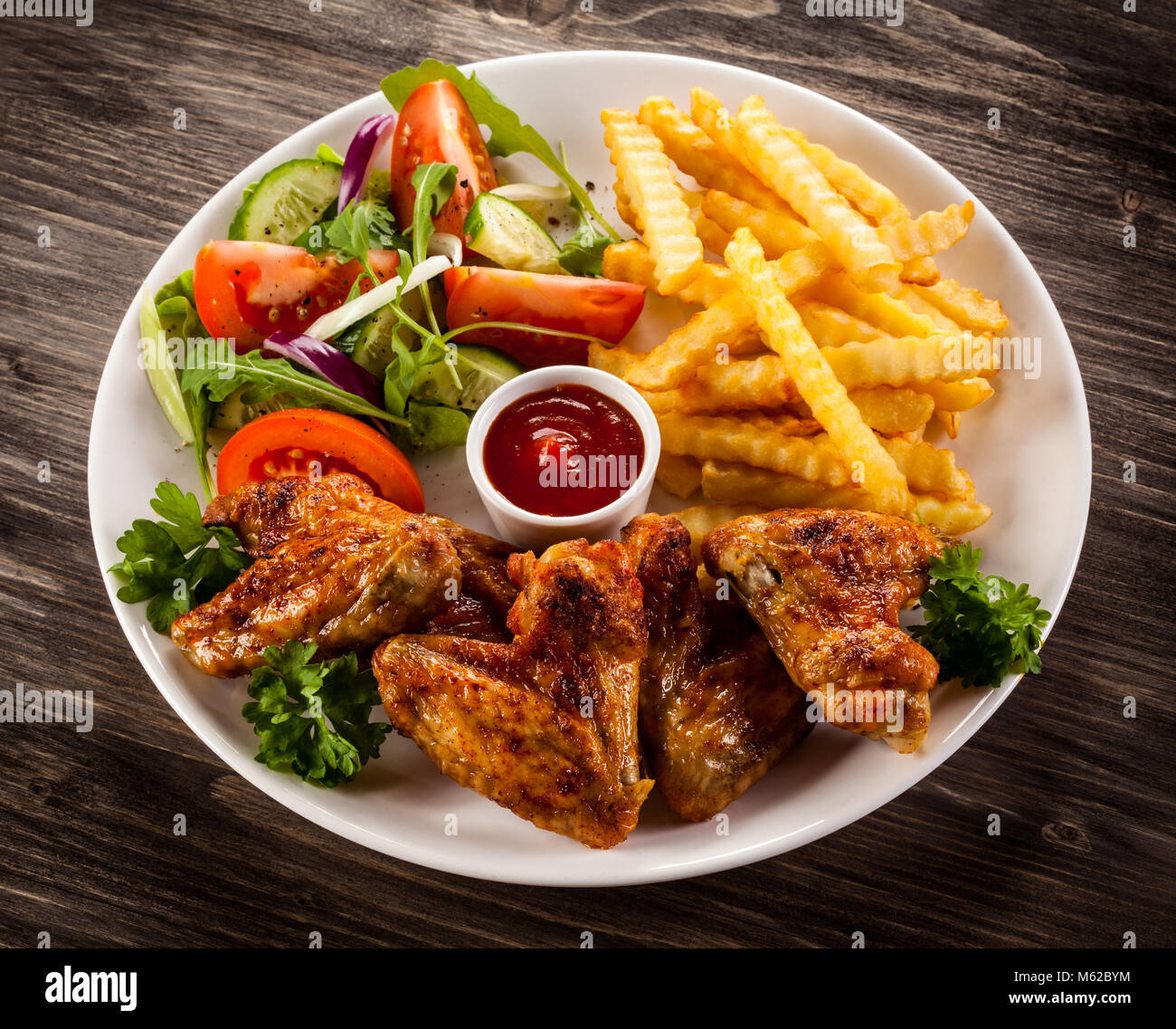 Grilled chicken wigs, chips and vegetables on wooden table Stock Photo ...