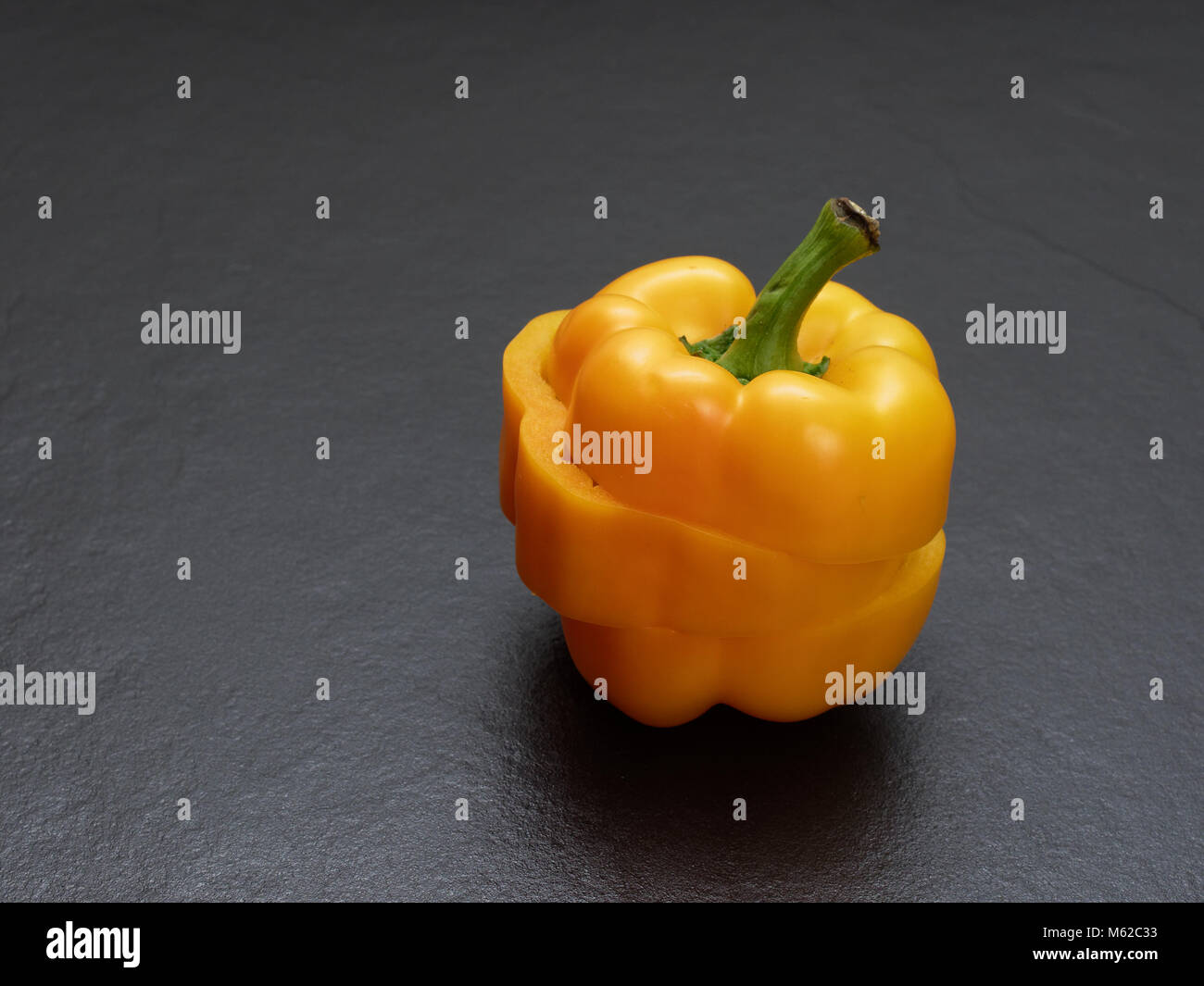 Yellow bell pepper or capsicum cut into three pieces over dark black ...