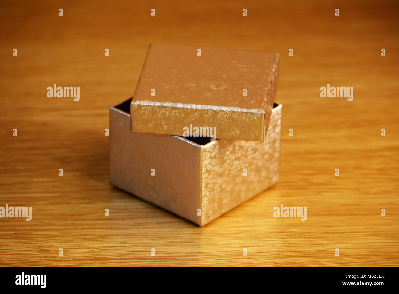 A small golden box on a light yellow wooden background. soft reflective ...