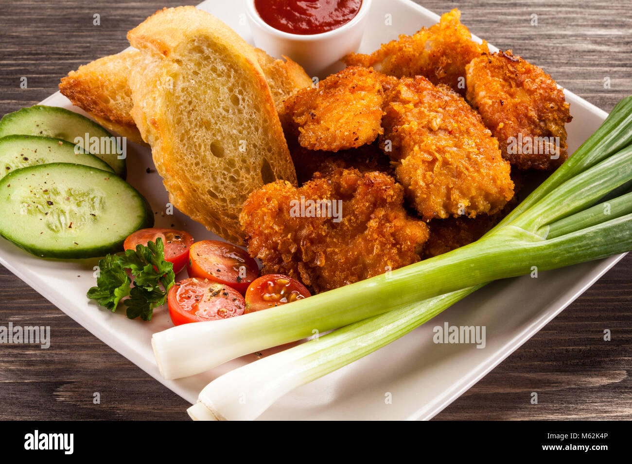 Grilled chicken nuggets and vegetables on wooden table Stock Photo - Alamy