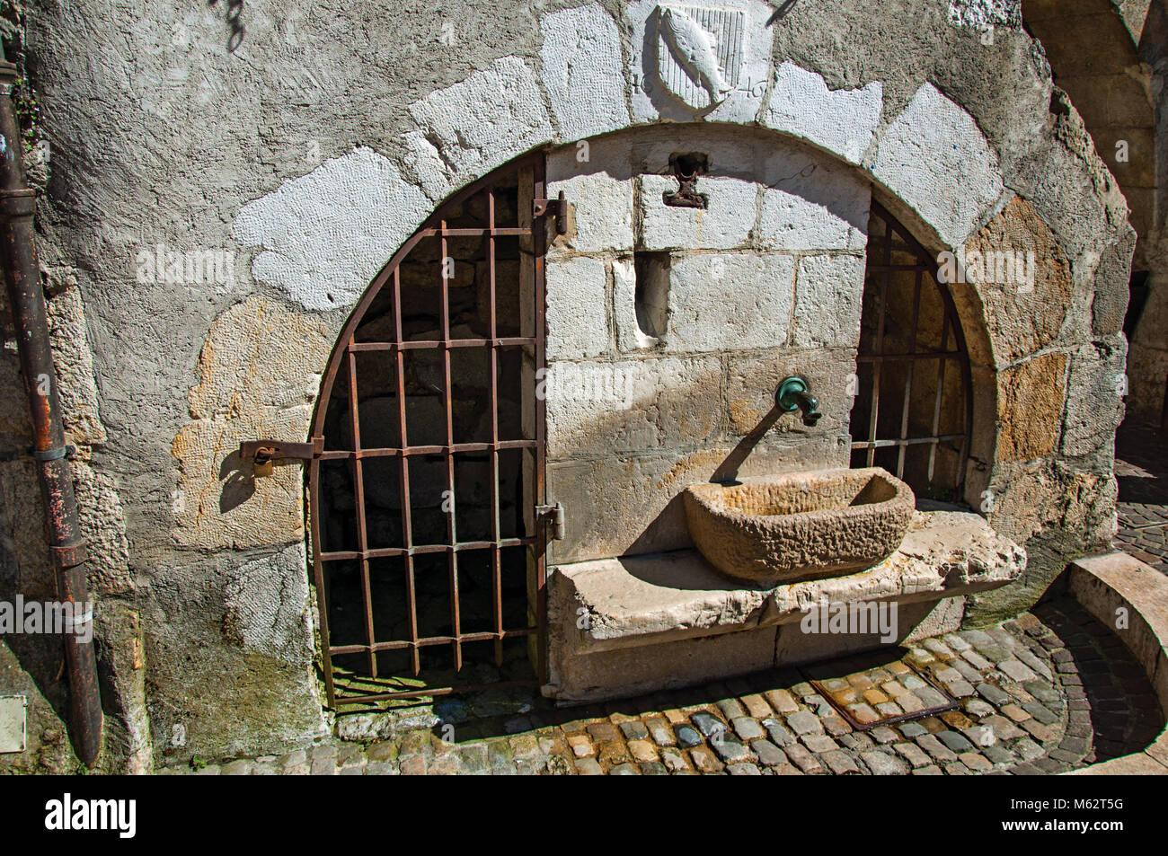 Old stone water fountain with iron gates and heraldic shield on the ...