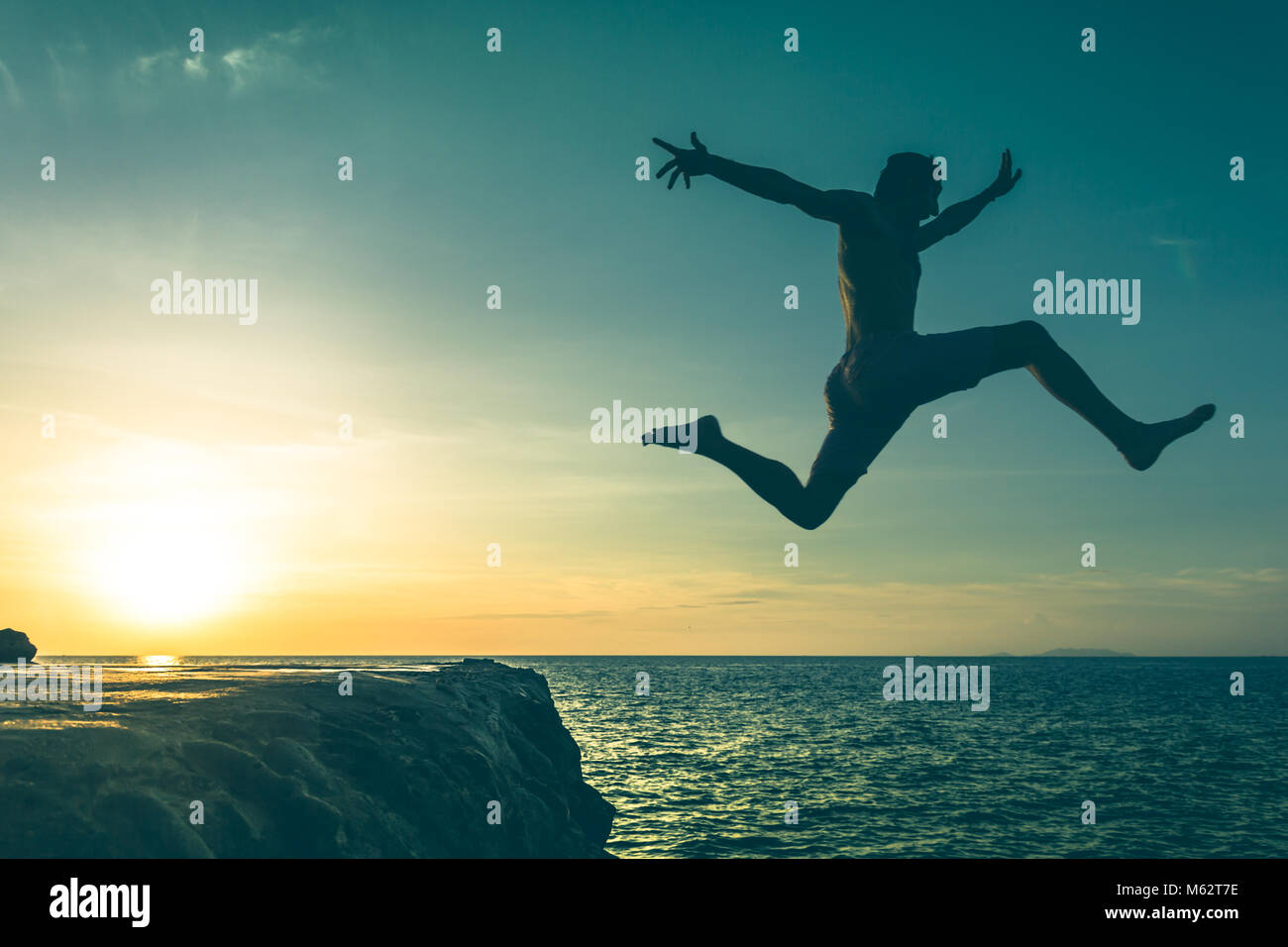 Man jumping over a cliff into the sea on sunset in Koh Phangan island ...