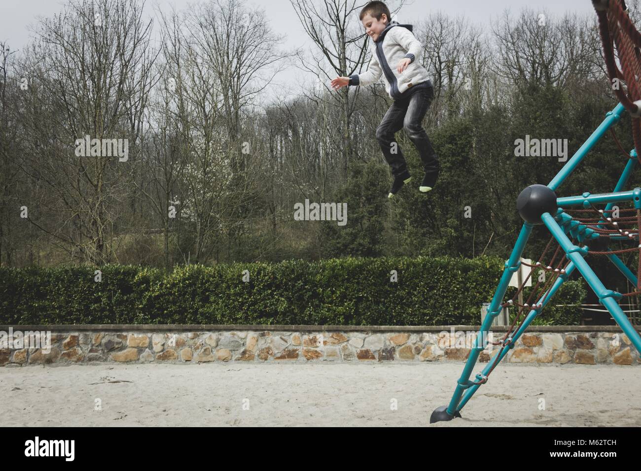 Smiling little kid high up in the air jumping from geometric structure ...