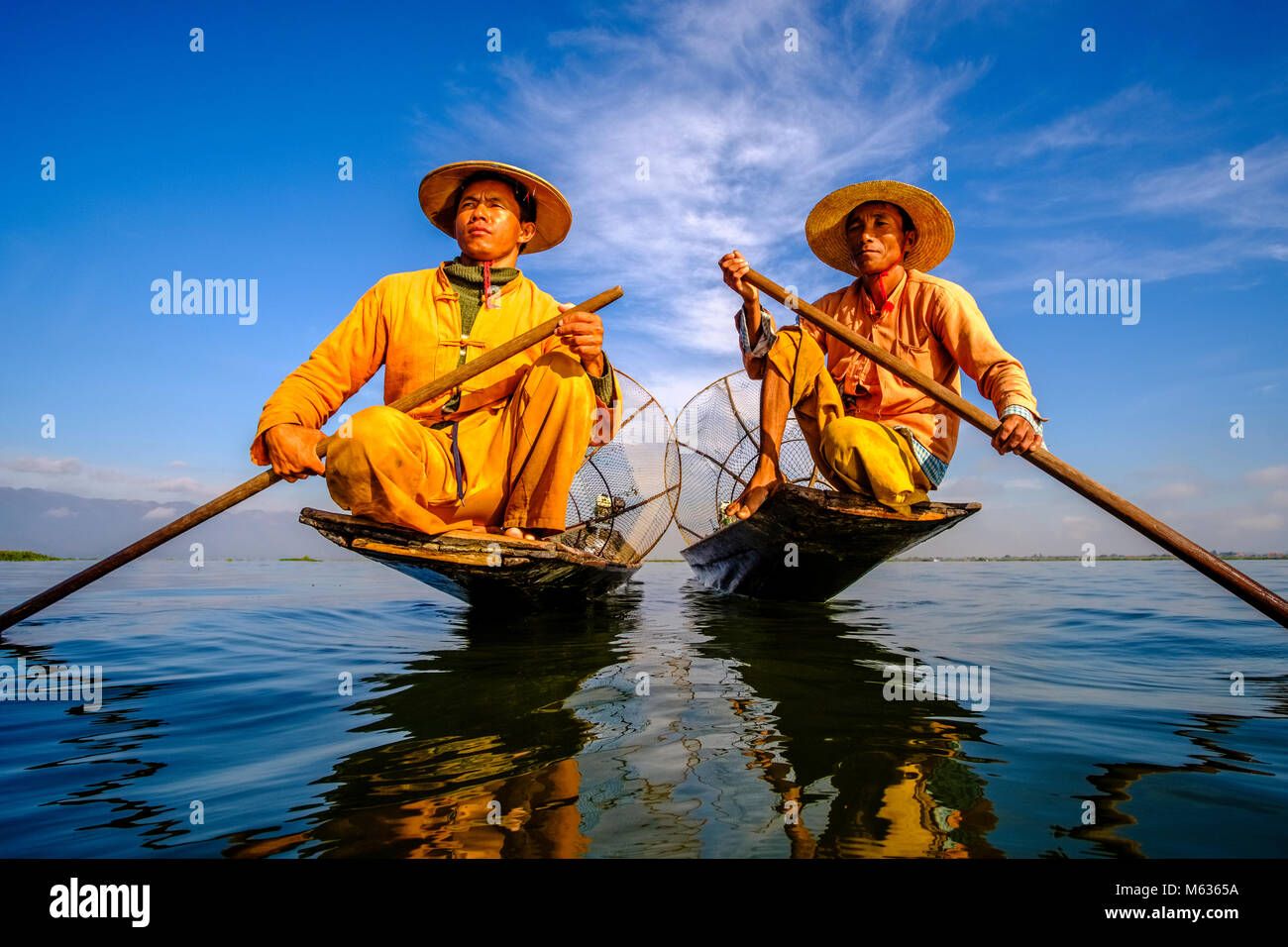 Two fishermen, sitting on their boats paddeling, are fishing the ...