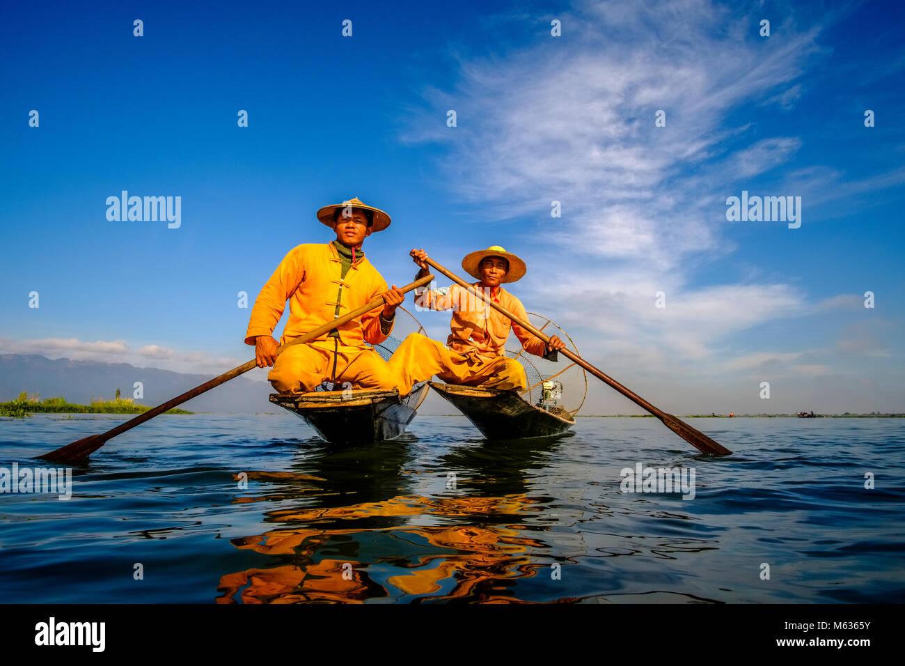 Two fishermen, sitting on their boats paddeling, are fishing the ...