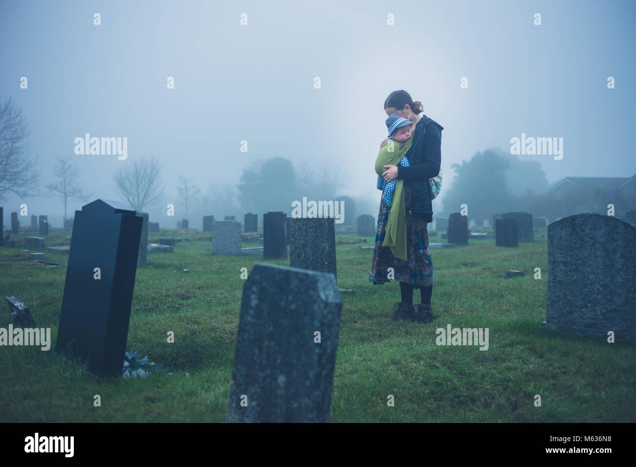 A grieving young mother is standing with her baby by a tombstone in a ...