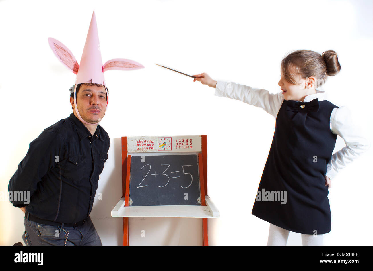 Little girl teaching mathematics to an adult dunce on little chalkboard ...