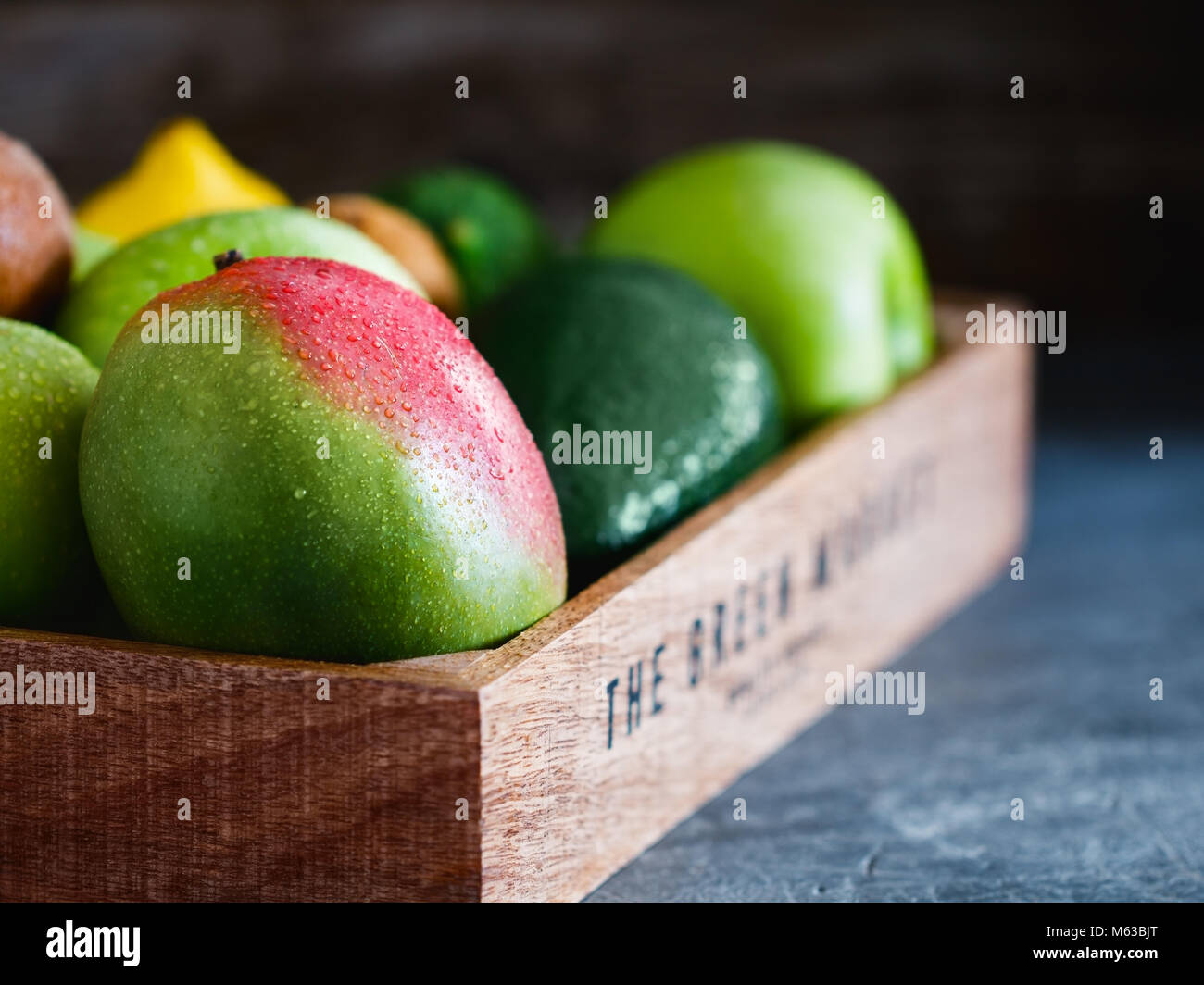 Wet fresh fruit and vegetables in a wooden box in a kitchen. The ...
