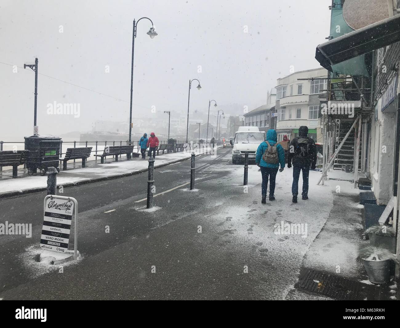 Cornwall, UK. 28th February, 2018. People walk across the harbour front ...