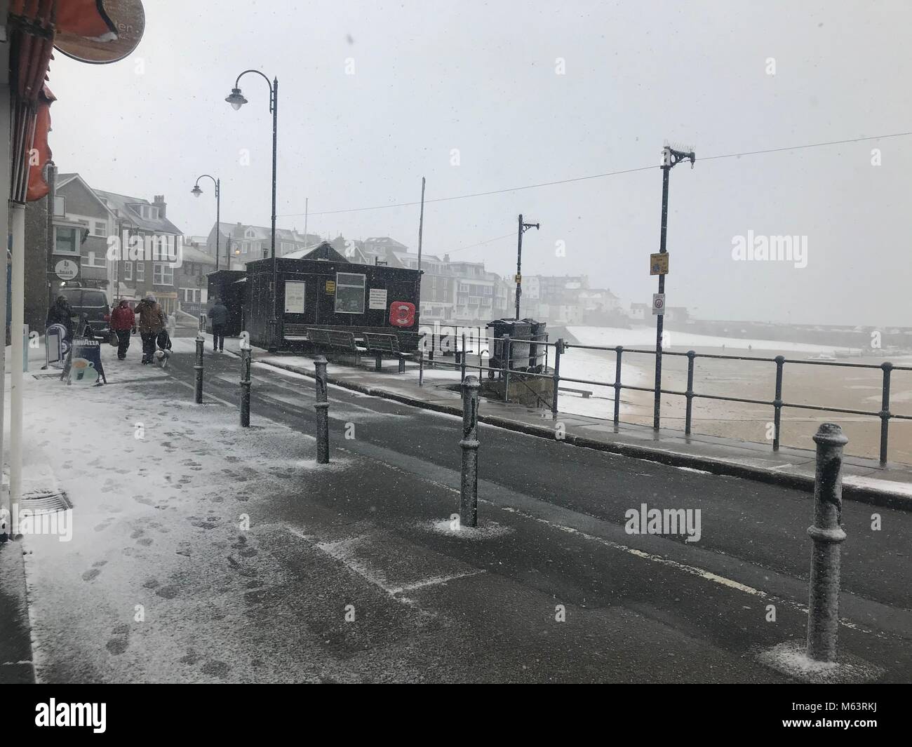 Cornwall, UK. 28th February, 2018. People walk across the harbour front ...