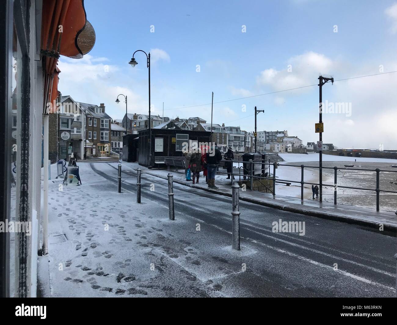 Cornwall, UK. 28th February, 2018. People walk across the harbour front ...