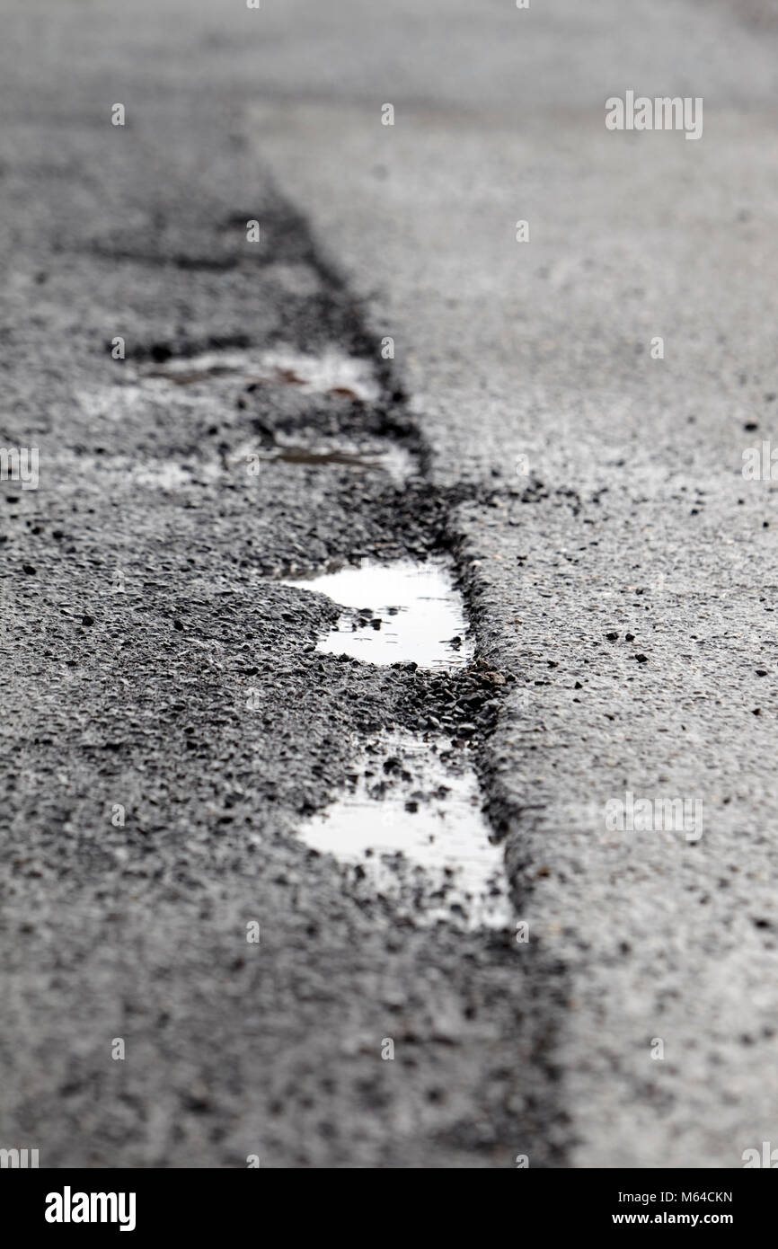 potholes forming on a road in line between new and old tarmac on street ...