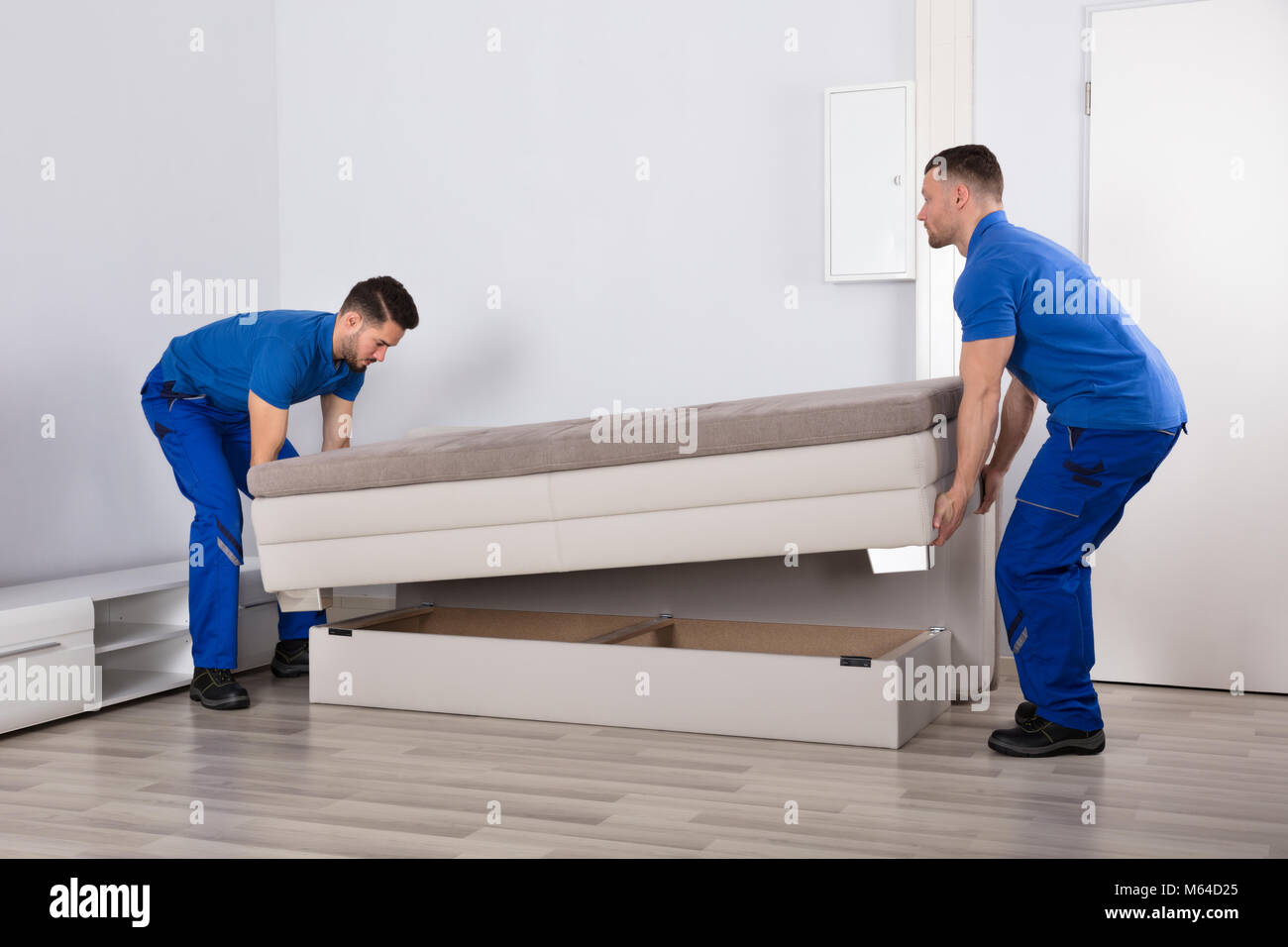 Two Young Men In Uniform Holding Sofa In Living Room Stock Photo - Alamy
