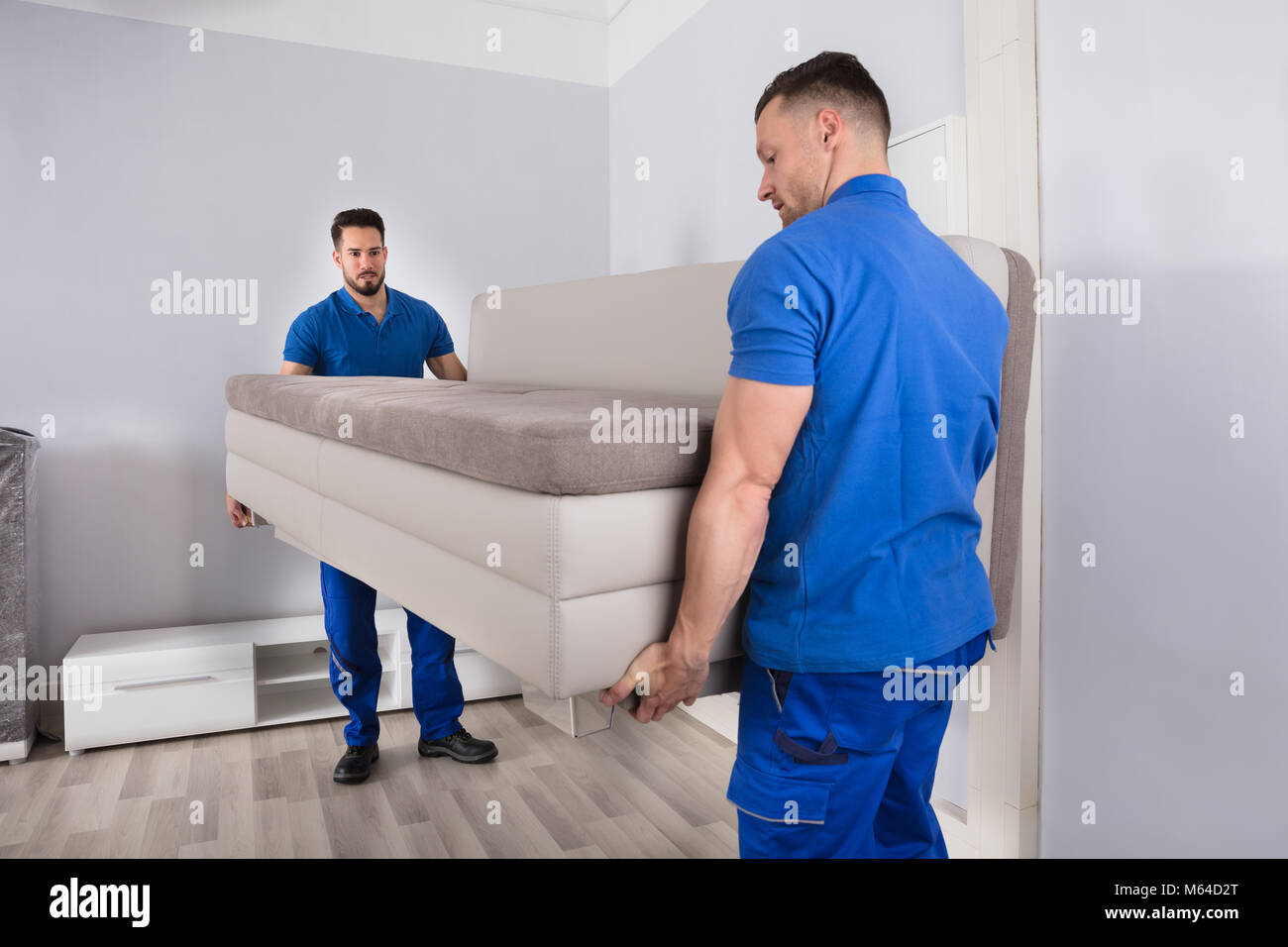 Two Young Men In Uniform Holding Sofa In Living Room Stock Photo - Alamy