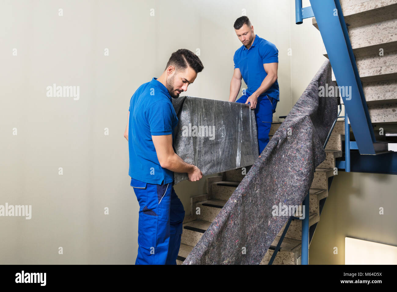 Two Young Male Movers In Uniform Carrying Furniture On Staircase Stock ...