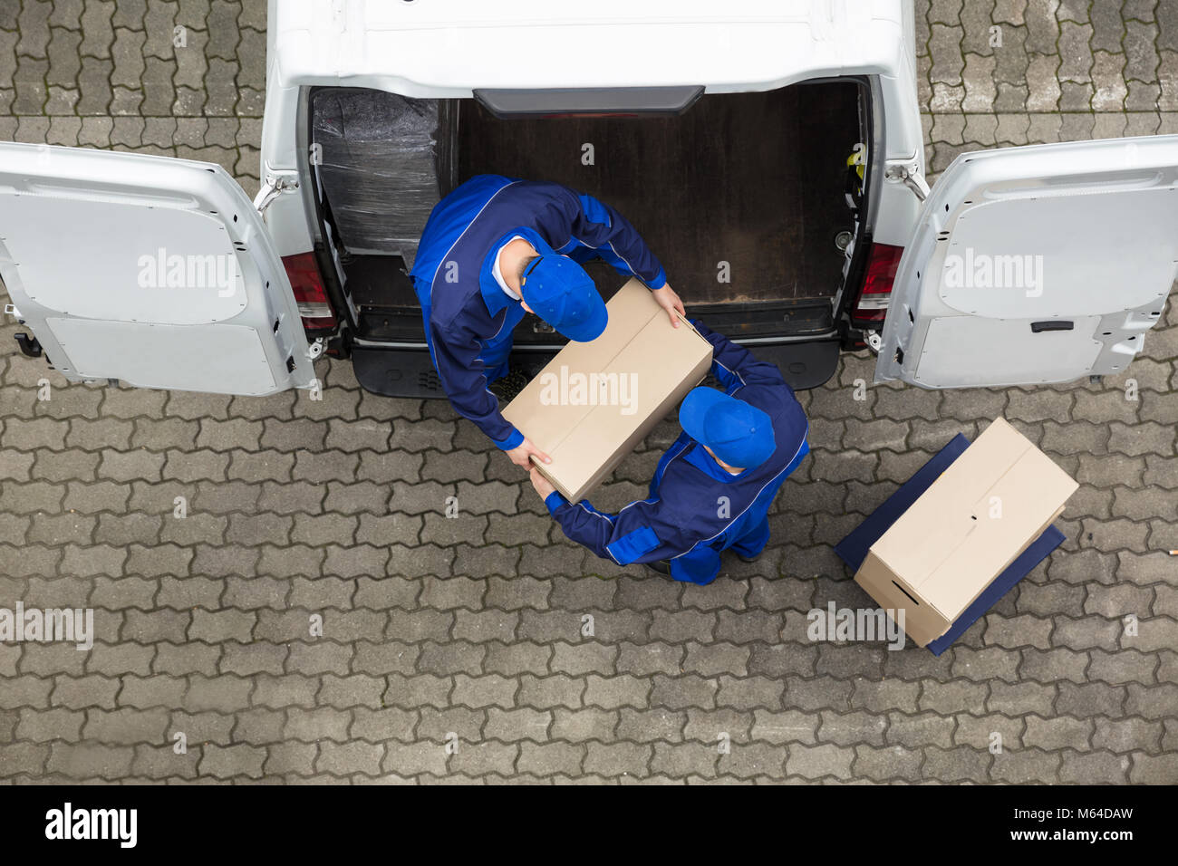 High Angle View Of Two Delivery Men Unloading Cardboard Box From Truck ...