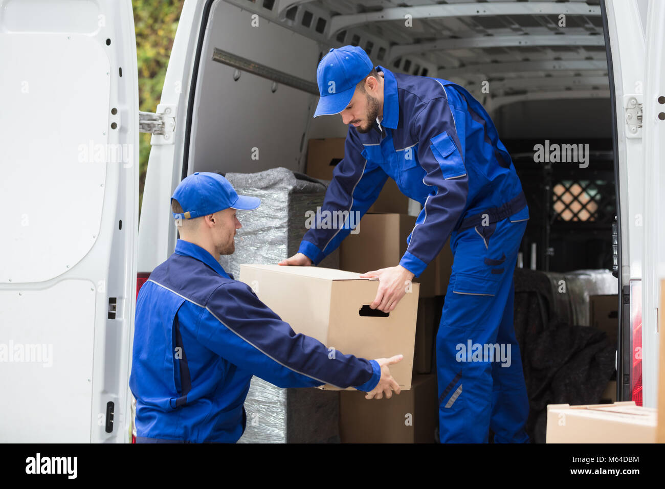 Two Young Male Movers Carrying Cardboard Box From Truck Stock Photo - Alamy