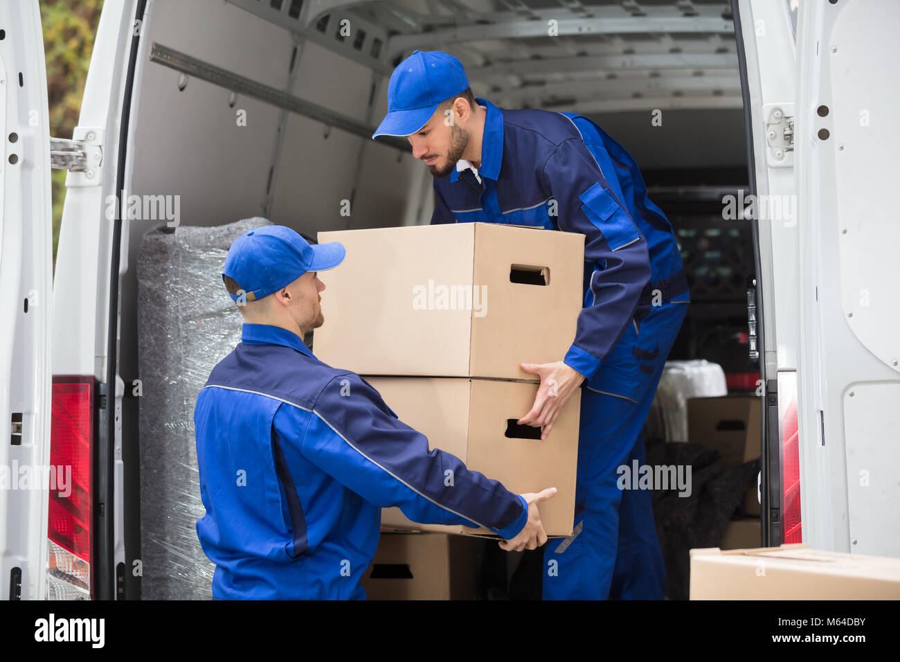 Two Young Male Movers Carrying Cardboard Box From Truck Stock Photo - Alamy