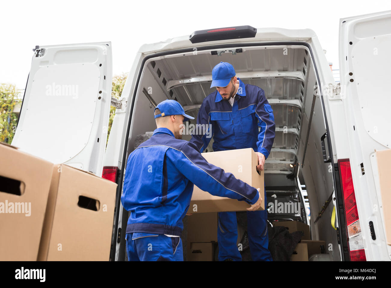 Two Young Male Movers Carrying Cardboard Box From Truck Stock Photo - Alamy