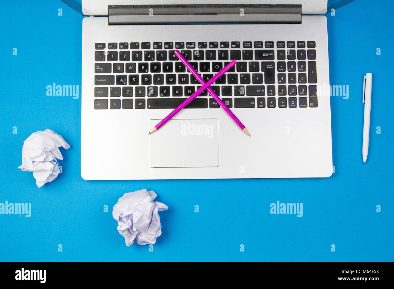 Laptop computer, cross pencils and crumpled paper on blue background ...