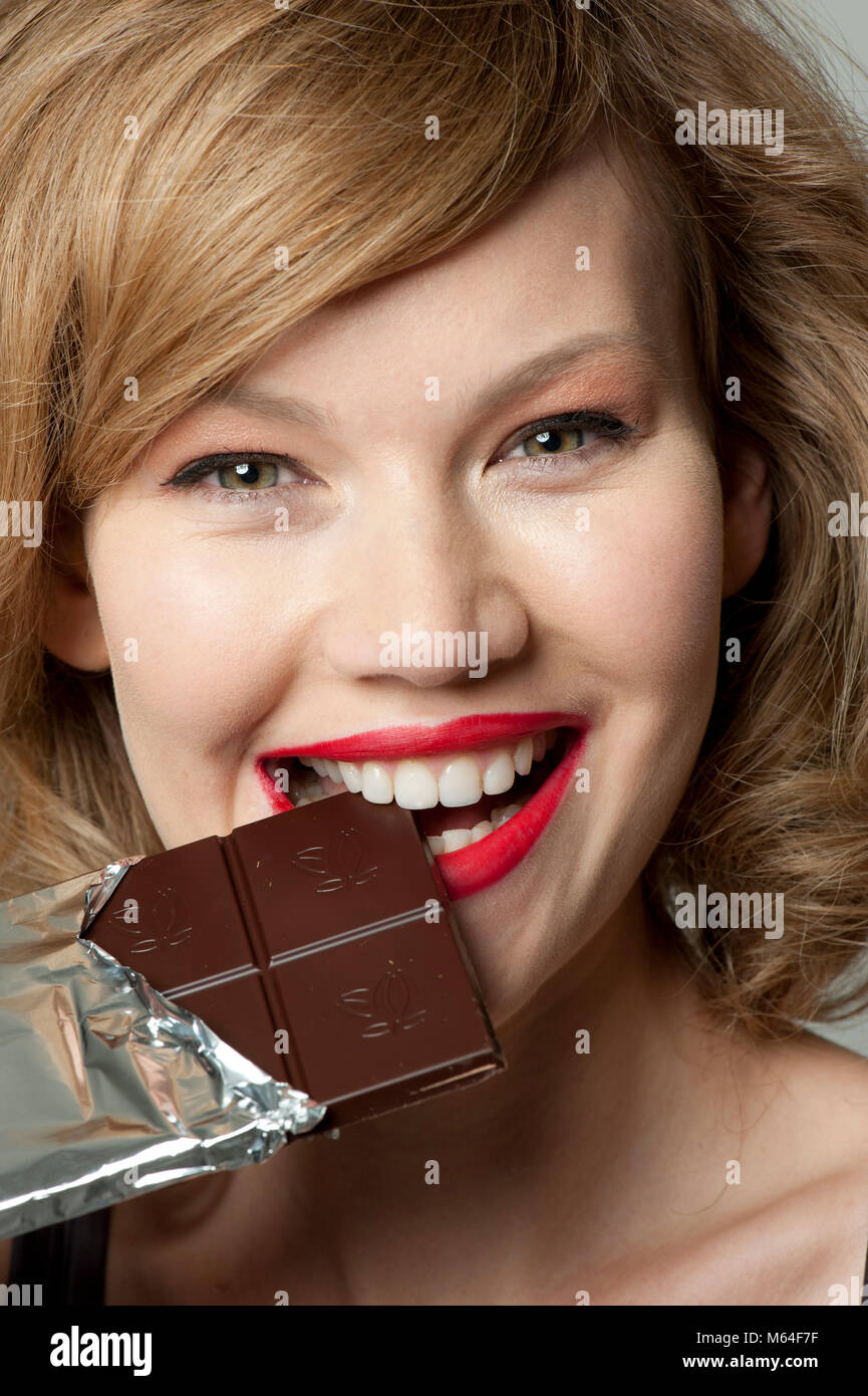 Happy woman biting into bar of dark chocolate Stock Photo - Alamy