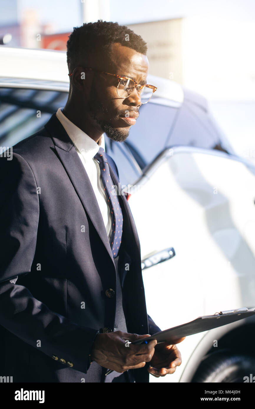 Handsome african car salesman standing at the dealership holding a ...