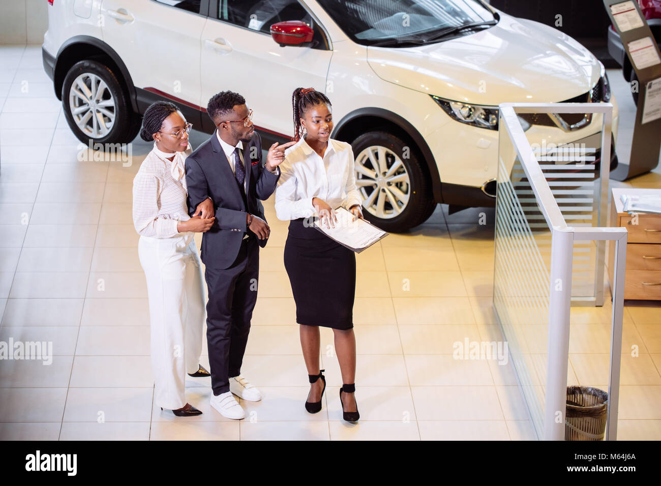 car salesman standing at dealership telling about features of car to ...