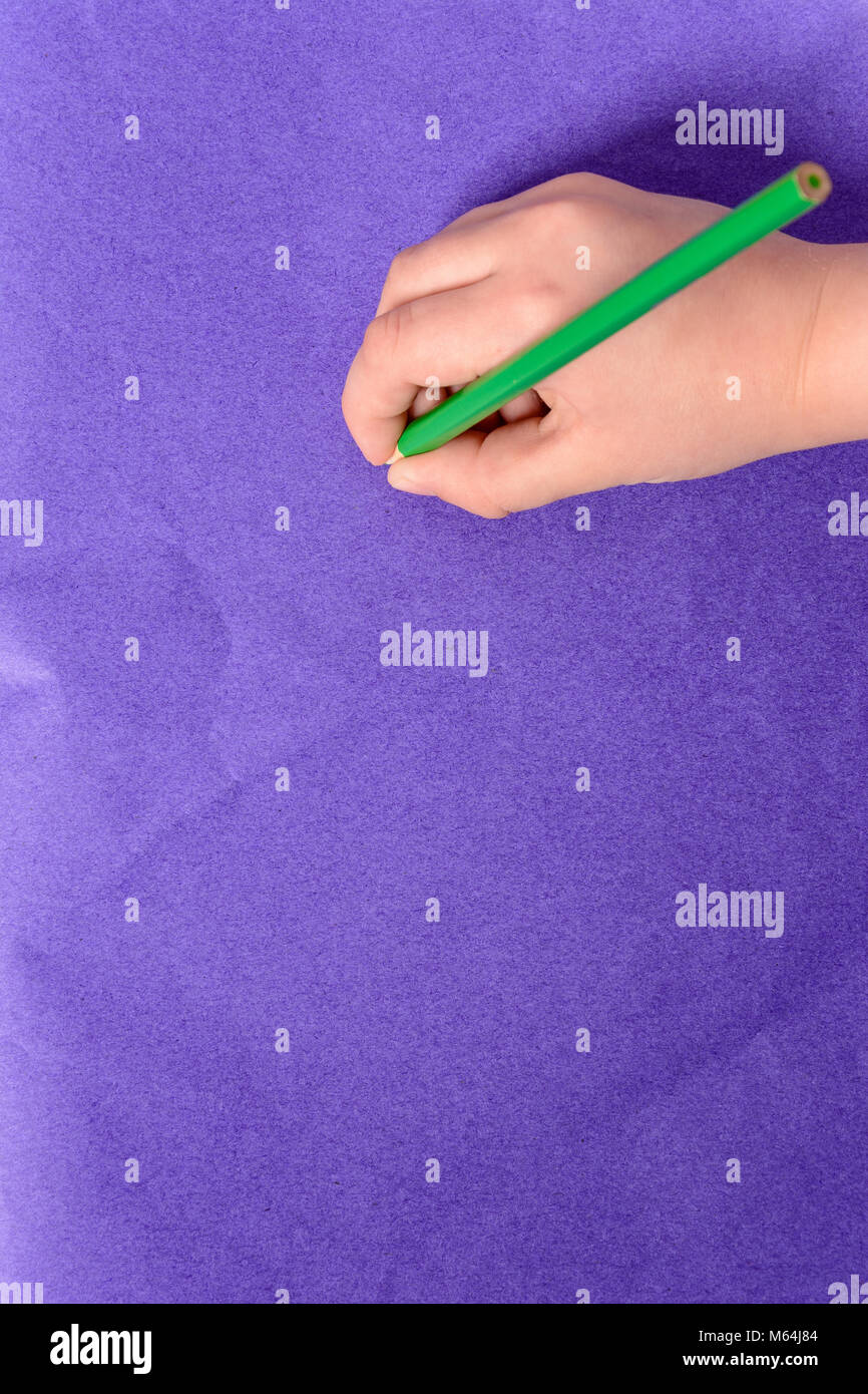 A photo of the hands of a young boy holding pencils and pens on colored ...
