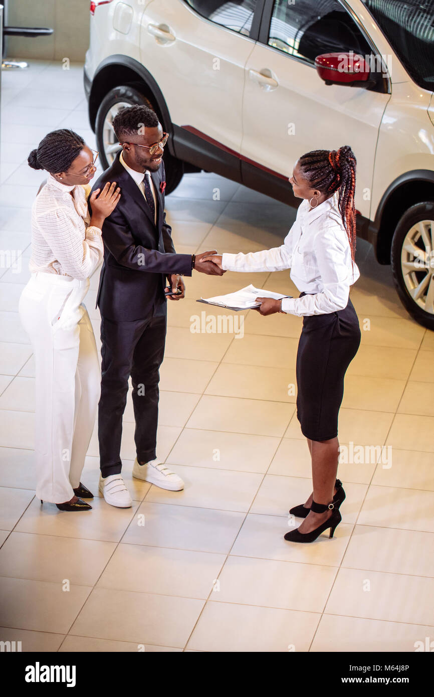 car salesman standing at dealership telling about features of car to ...