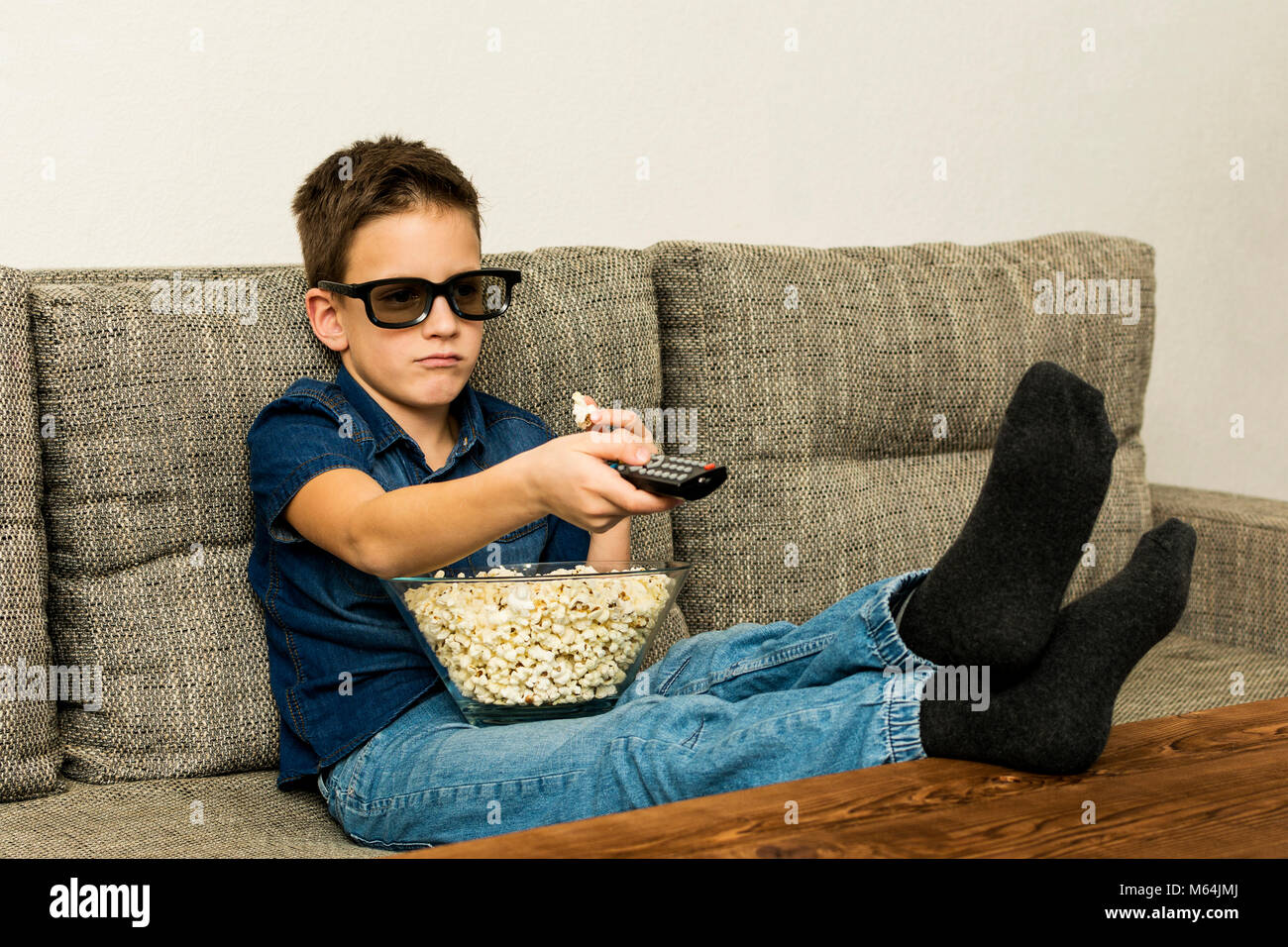 Small boy on the couch watching TV and eating popcorn? Legs on table ...