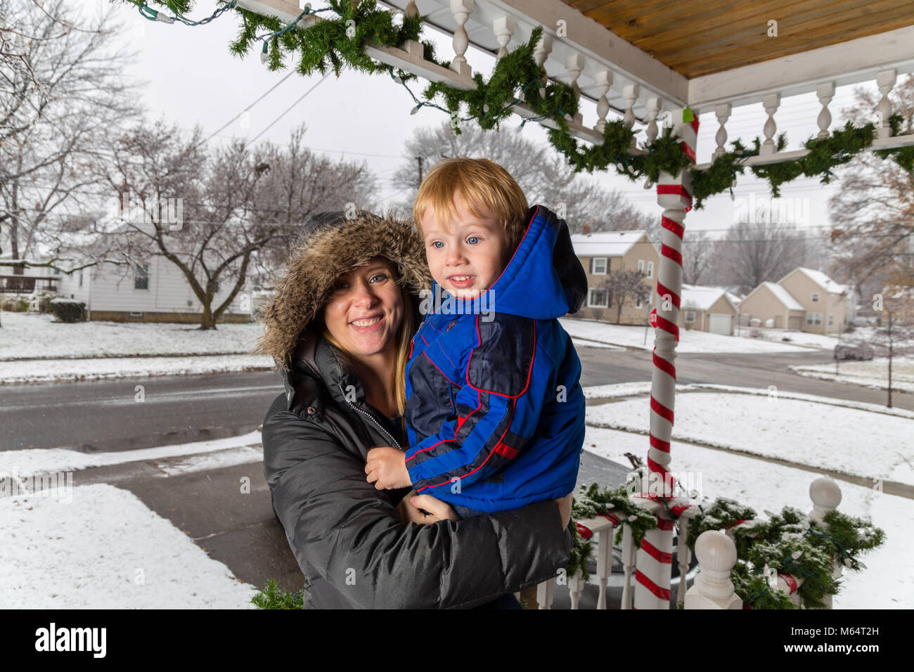 A Young Caucasian Mom Lifts Her Son In The Air On A Christmas Decorated