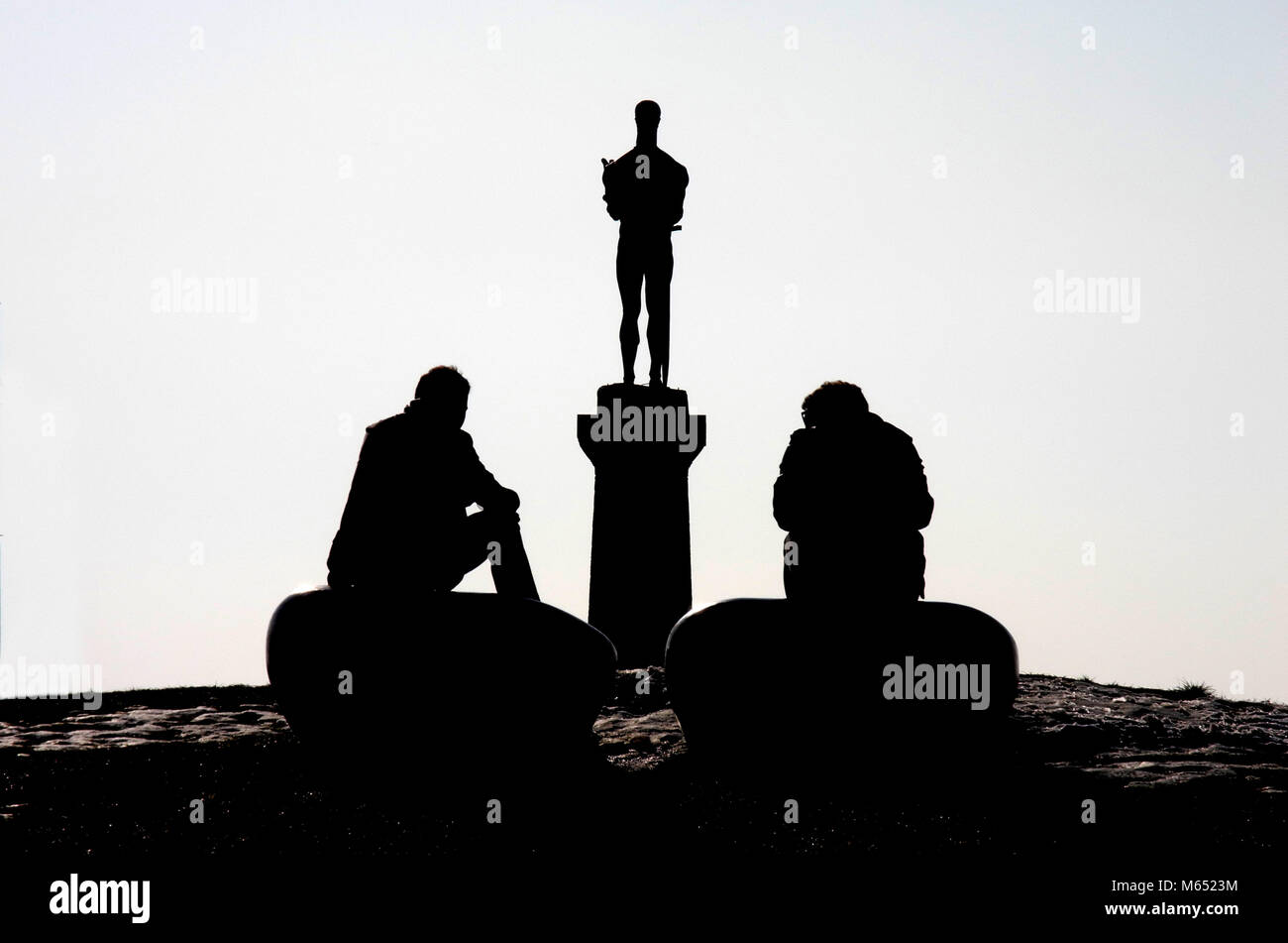 Two men sitting in front of statue of Pobednik in Belgrade at sunset ...