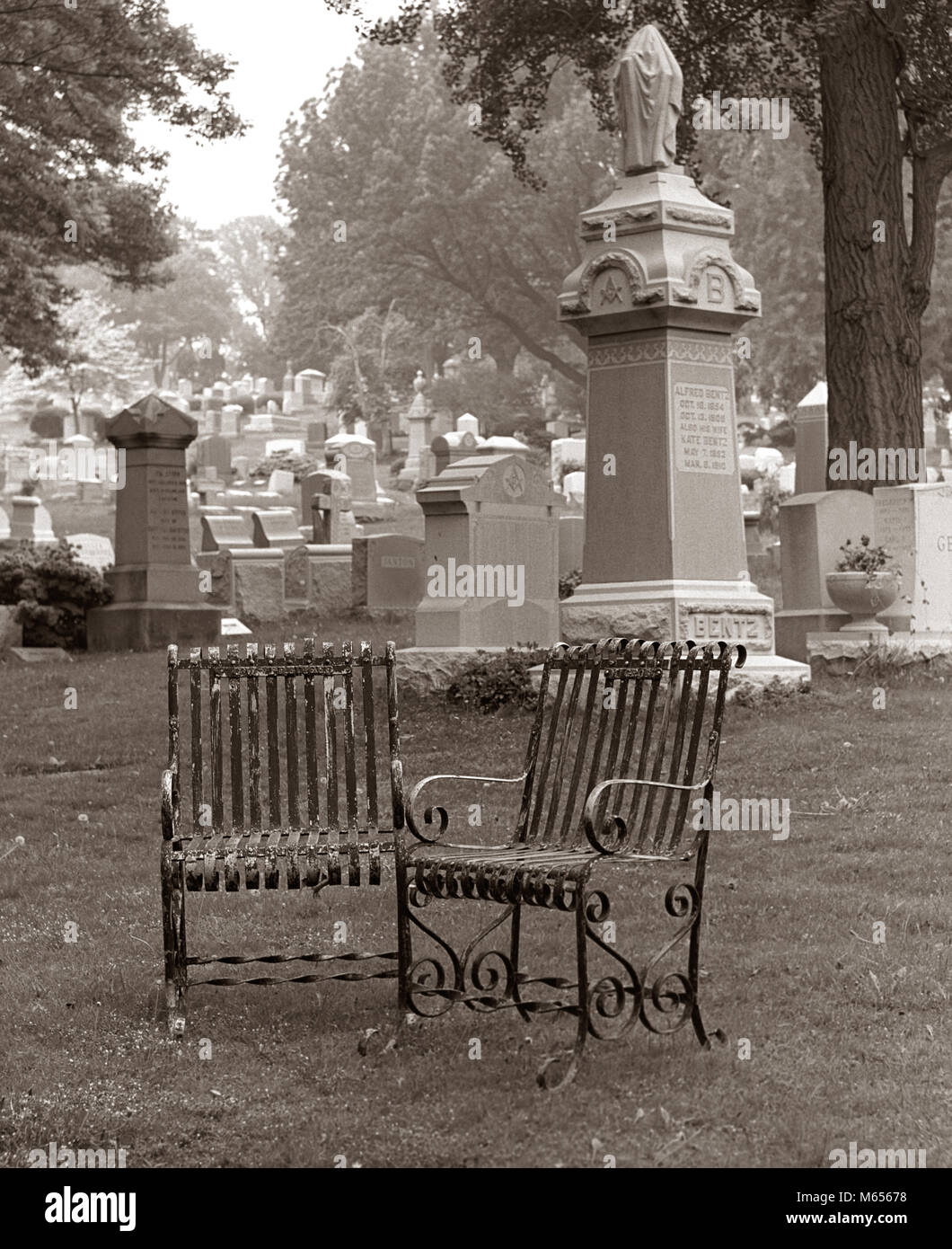 1970s TWO EMPTY RUSTY WROUGHT IRON CHAIRS TOGETHER ON GRASS IN CEMETERY ...