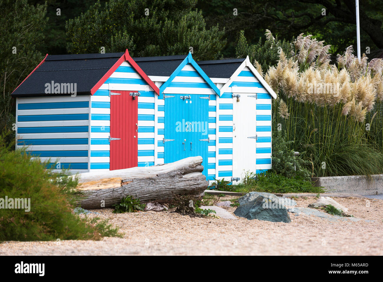 Three beach huts with blue stripes on the edge of a beach in the UK ...