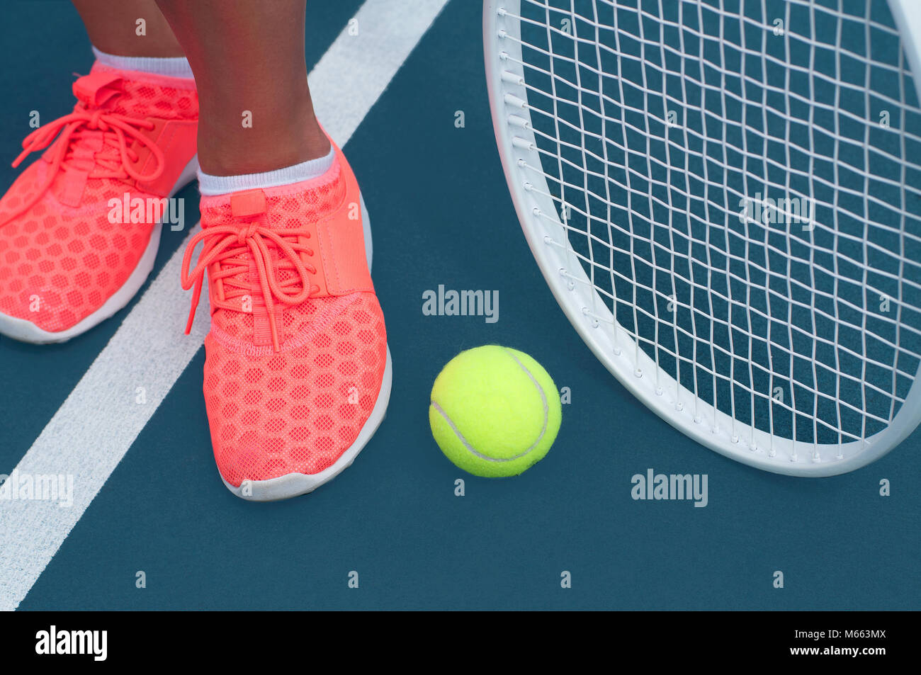 Female feet in sneakers with tennis ball and racket on tennis court ...