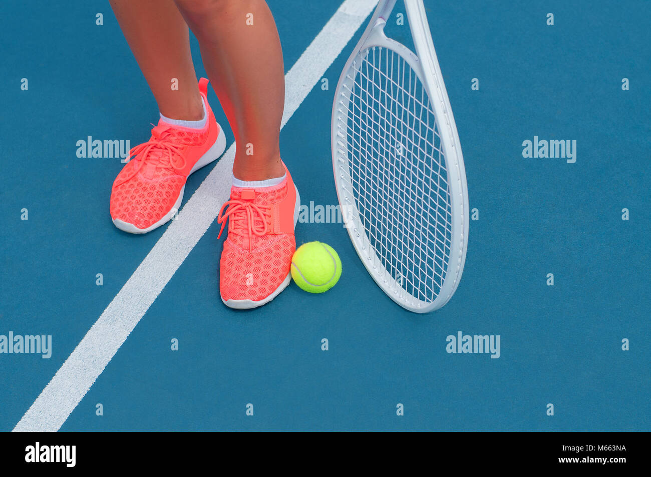 Female feet in sneakers with tennis ball and racket on tennis court ...