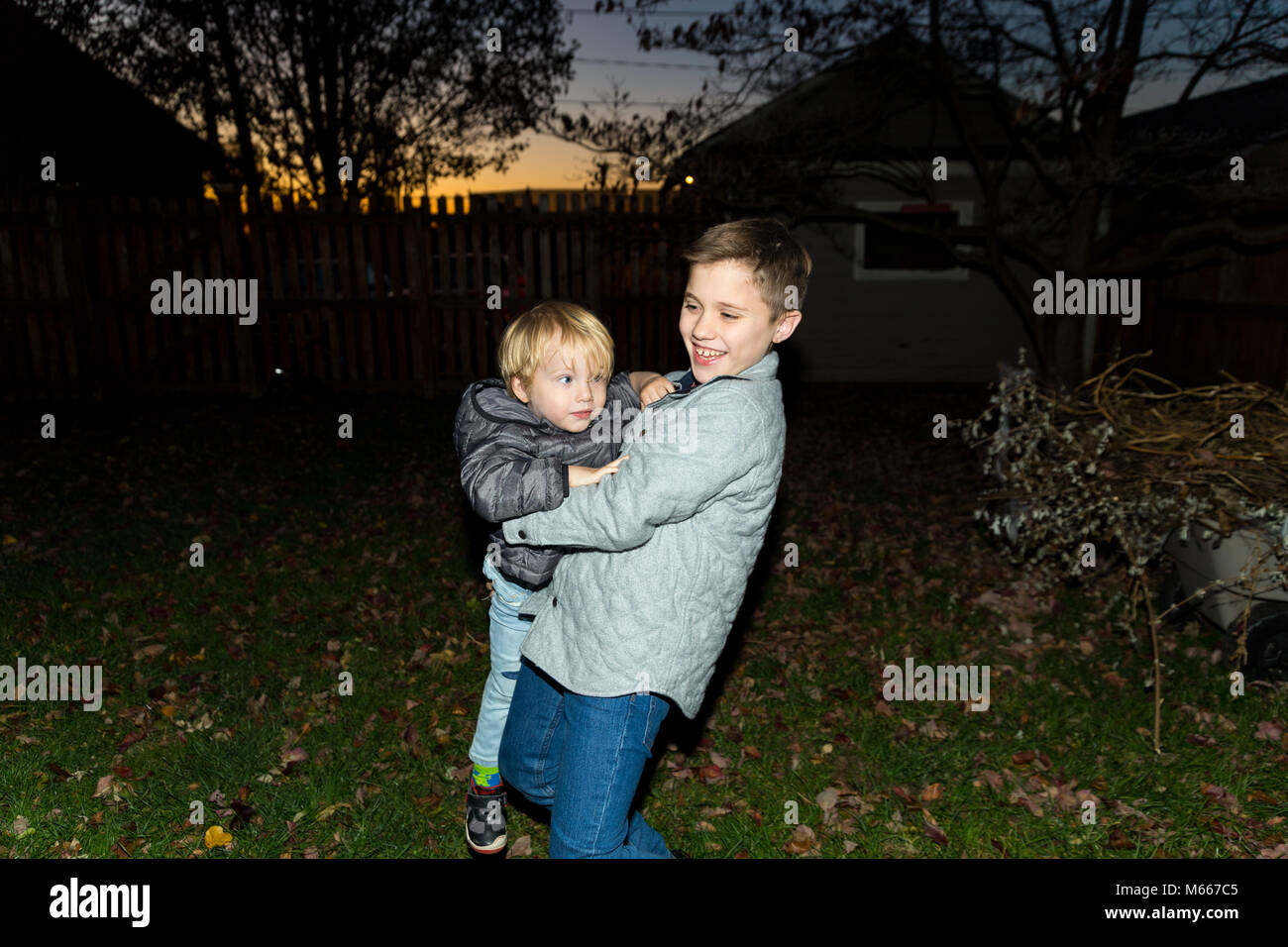 Two Young Boys Play With One Another In Their Backyard On A Cool Fall ...
