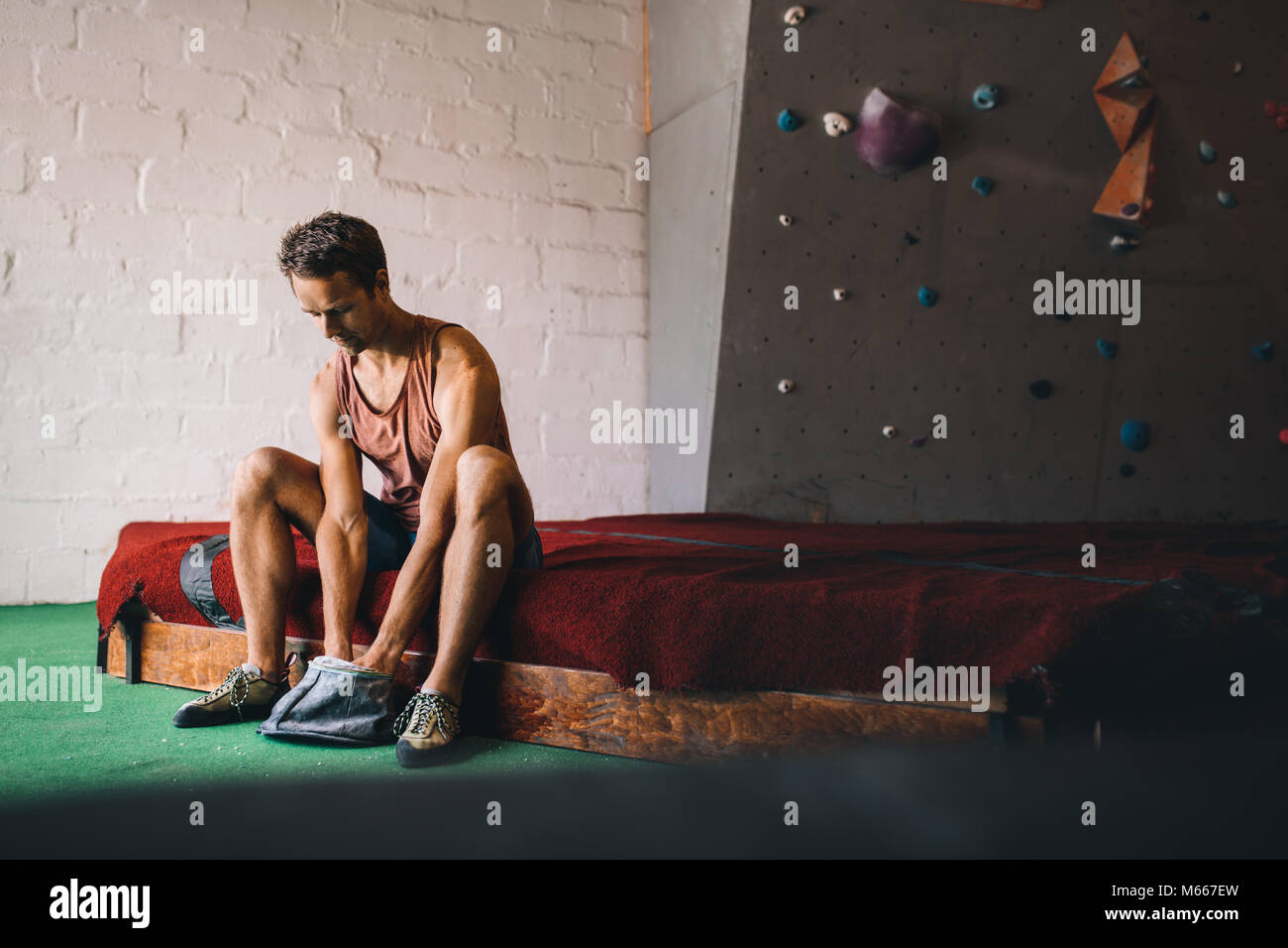 Man at a wall climbing gym applying magnesium chalk powder on hands ...