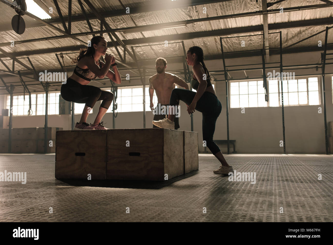 Group of people jumping on wooden boxes in gym. Three people performing ...
